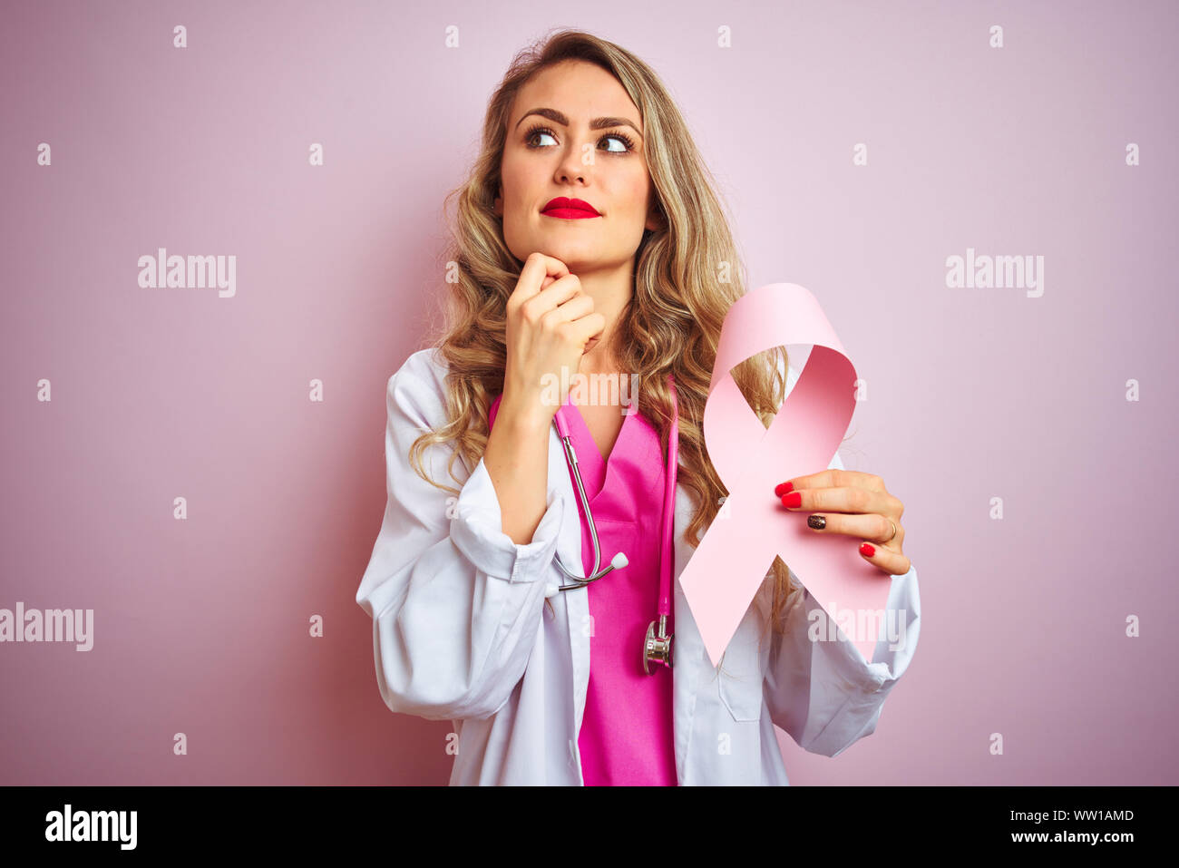 Young beautiful doctor woman holding cancer ribbon over pink isolated ...