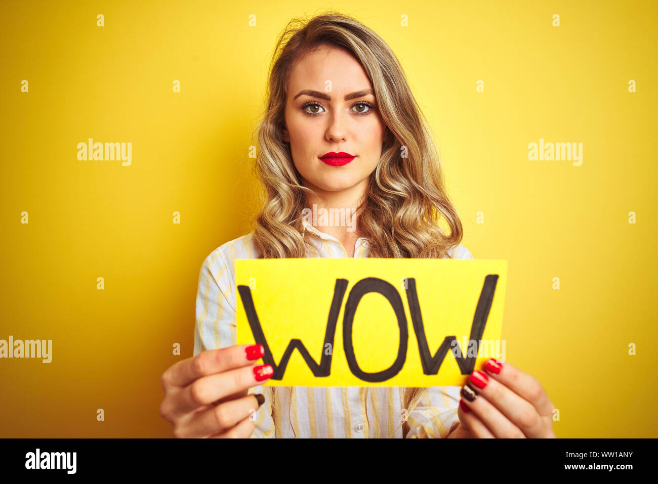 Beautiful woman holding amazed wow surprise banner over isolated yellow ...