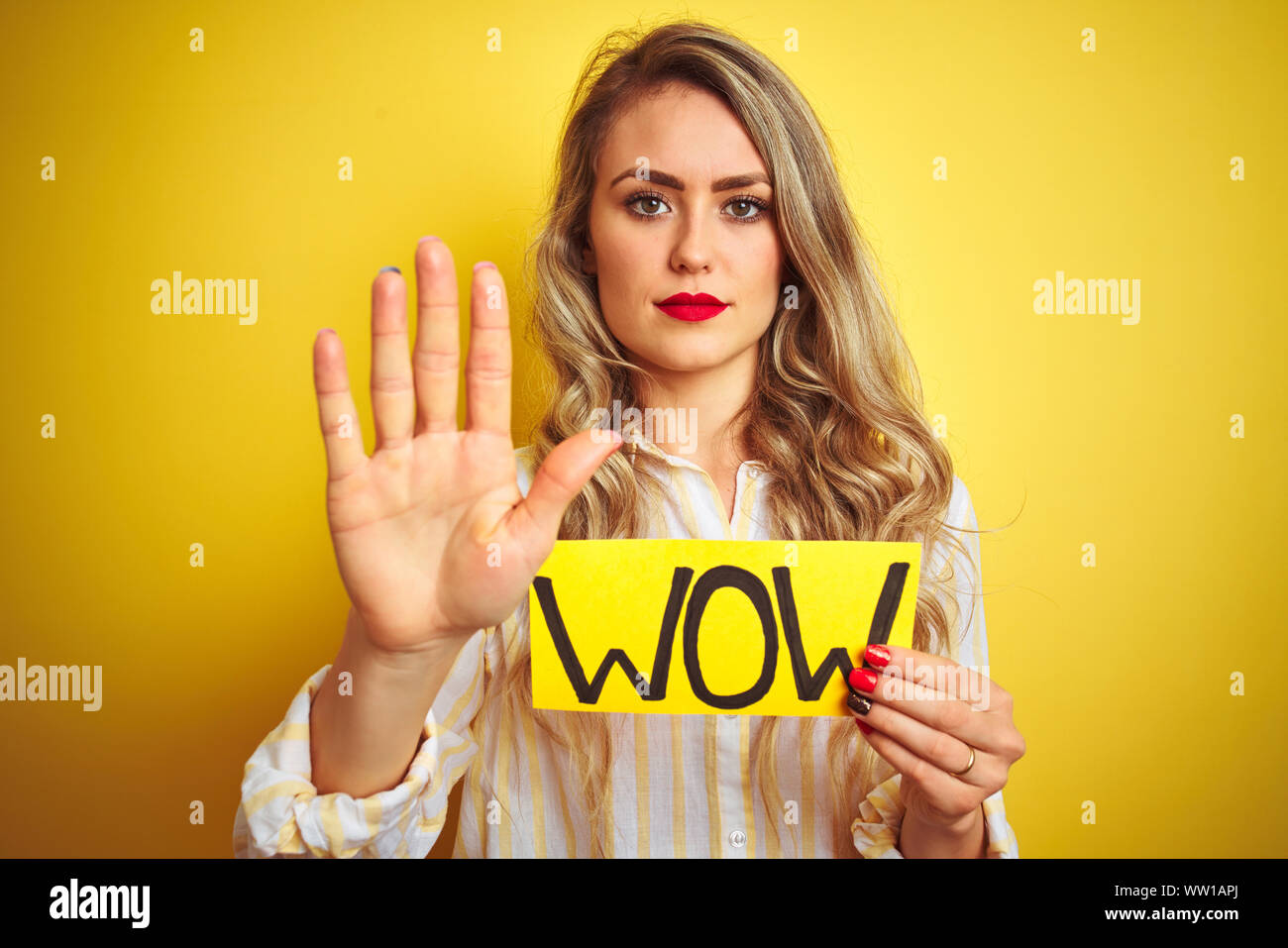 Beautiful woman holding amazed wow surprise banner over isolated yellow ...