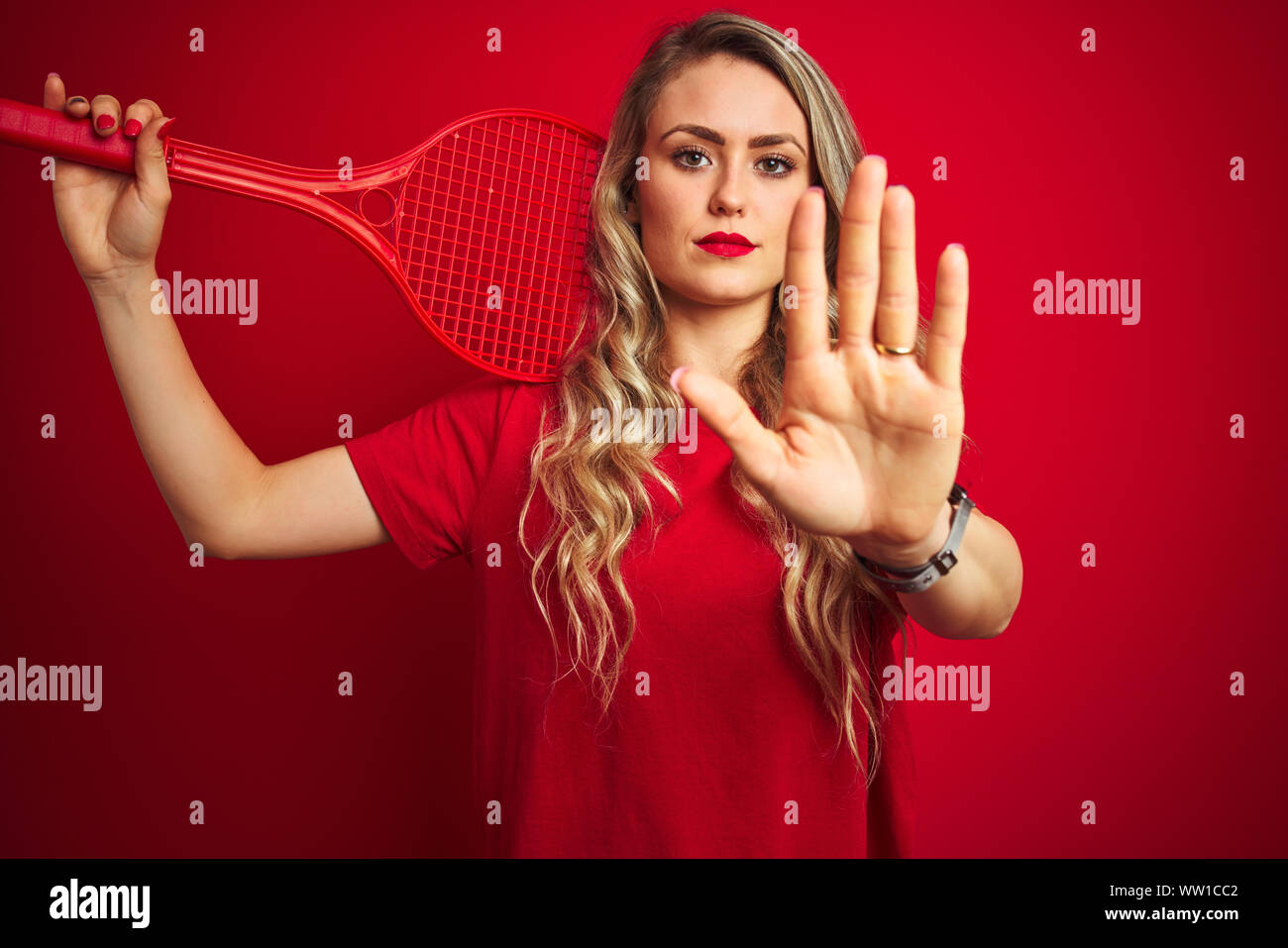 Young sportwoman playing tennis with racket and a ball over red ...