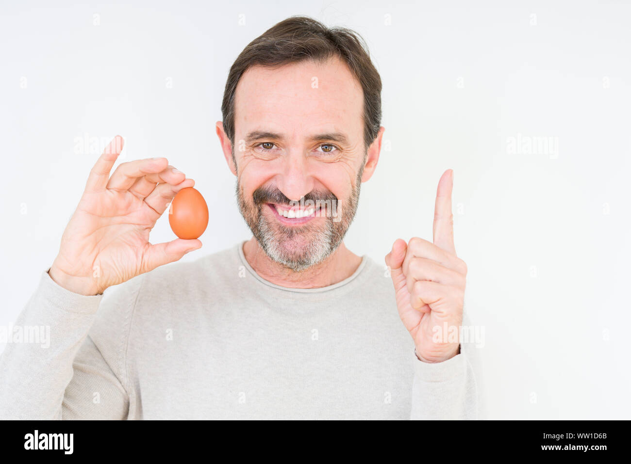 Senior man holding fresh egg over isolated background surprised with an ...