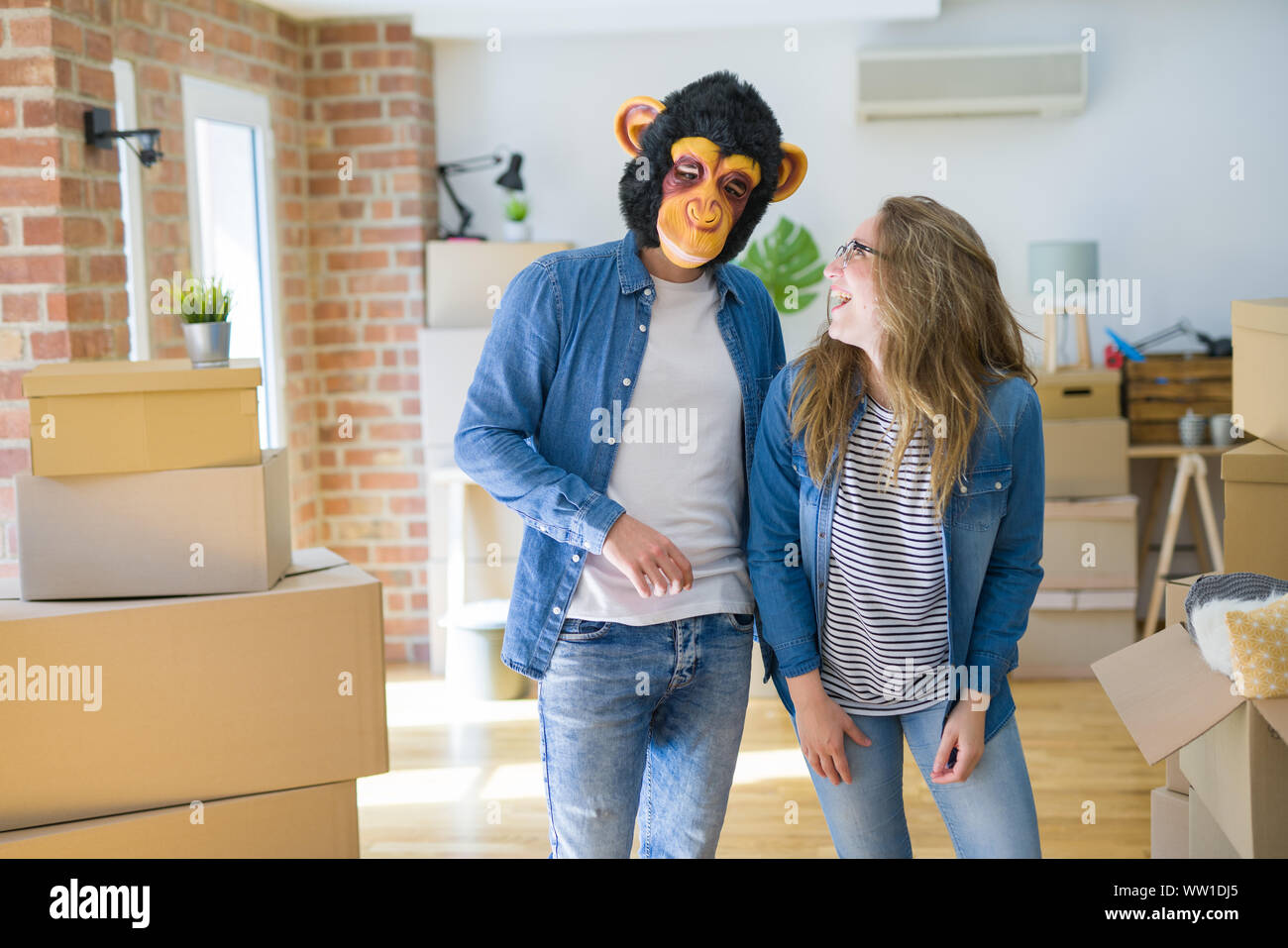 Young couple having fun wearing a monkey mask moving to a new apartment ...