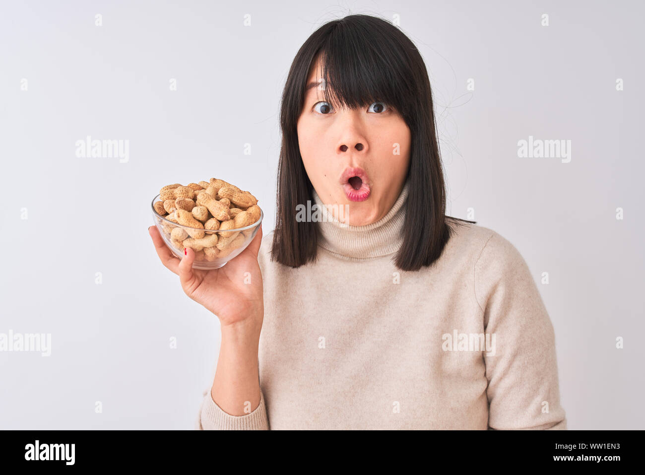 Young beautiful Chinese woman holding bowl with peanuts over isolated ...