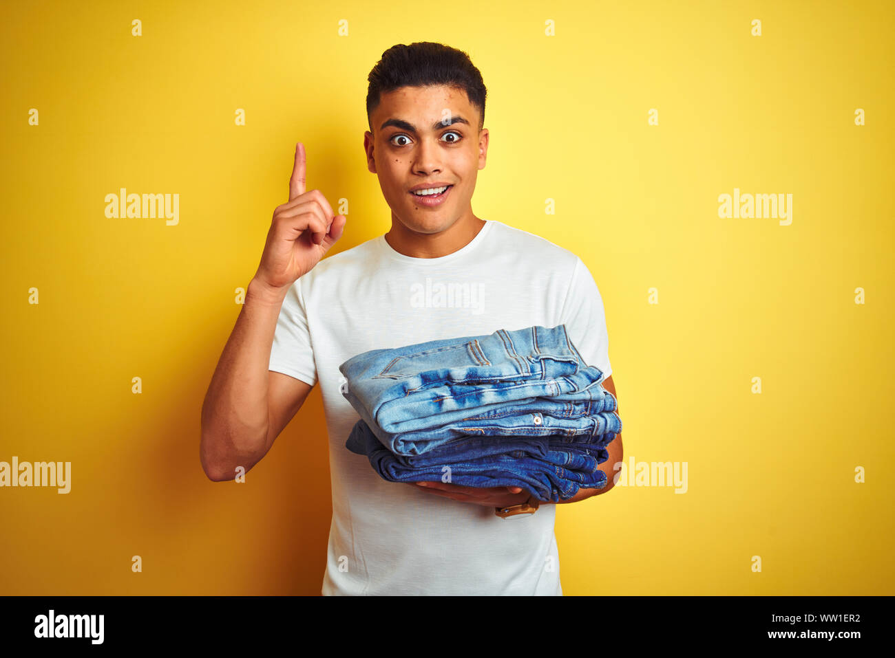 Young brazilian shopkeeper man holding jeans standing over isolated ...