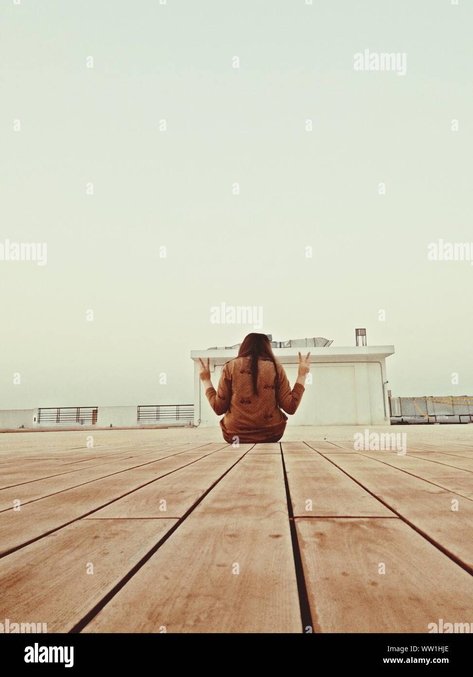 Rear View Of Woman Showing Peace Sign While Relaxing On Walkway Stock ...