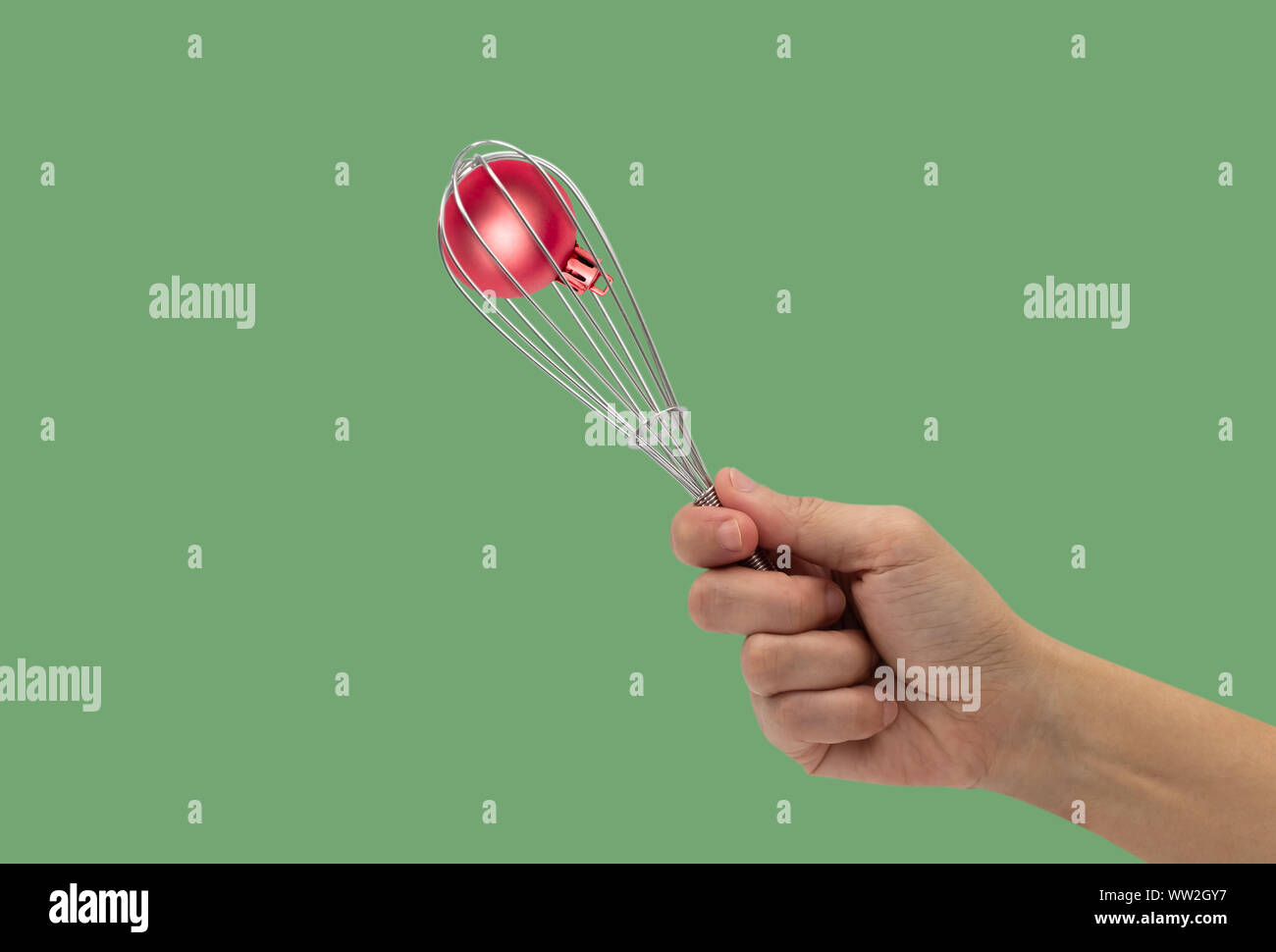 Female hand with a kitchen whisk and ball christmas isolated on green ...