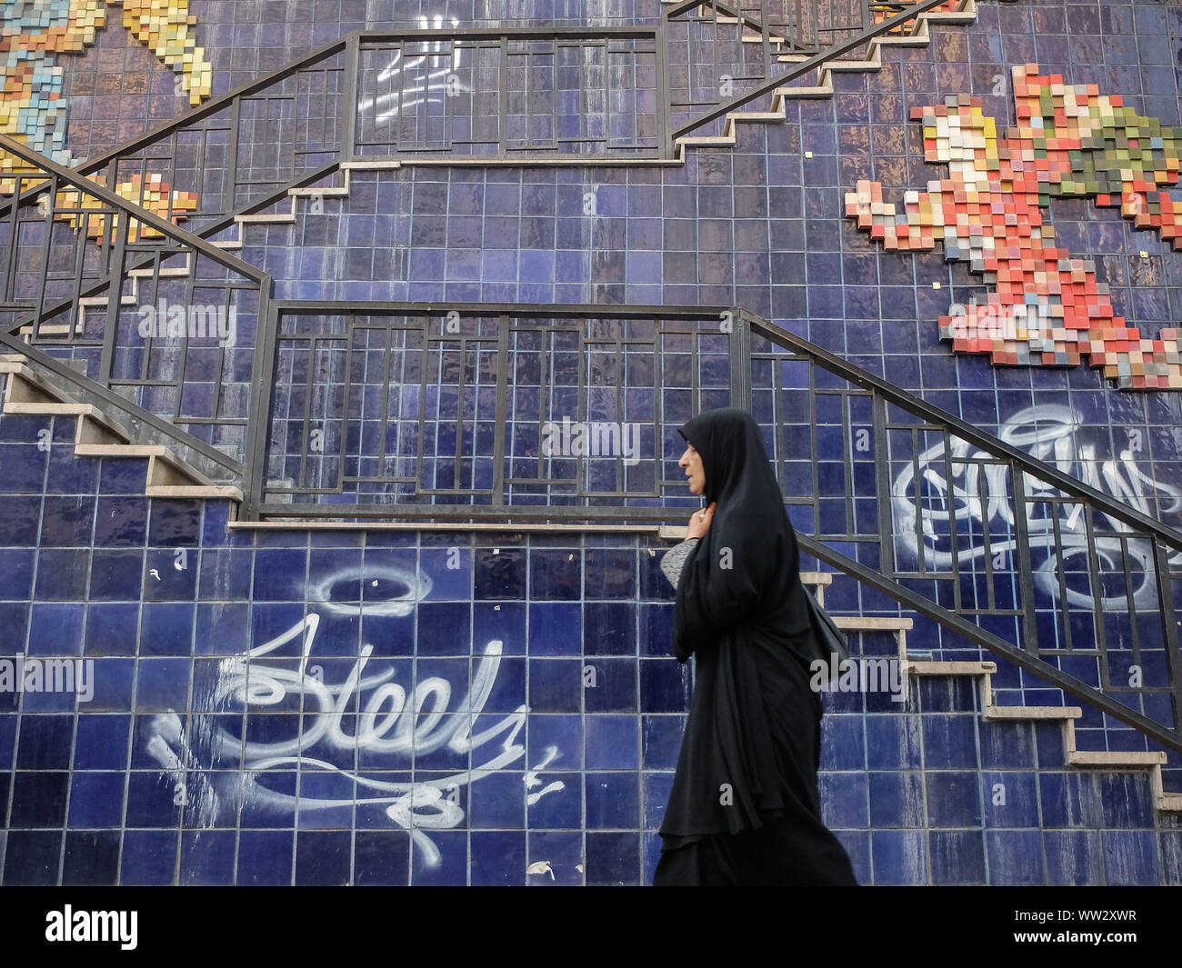 Tehran, Iran. 12th Sep, 2019. A veiled woman walks past a mural in a ...