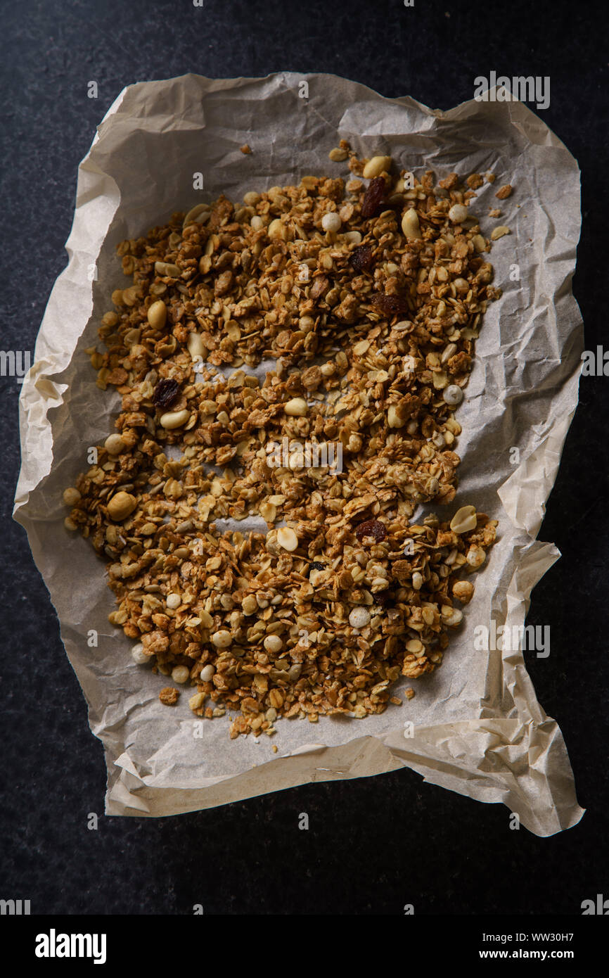 Top view of roasted granola with nuts, flakes and raisins on parchment ...