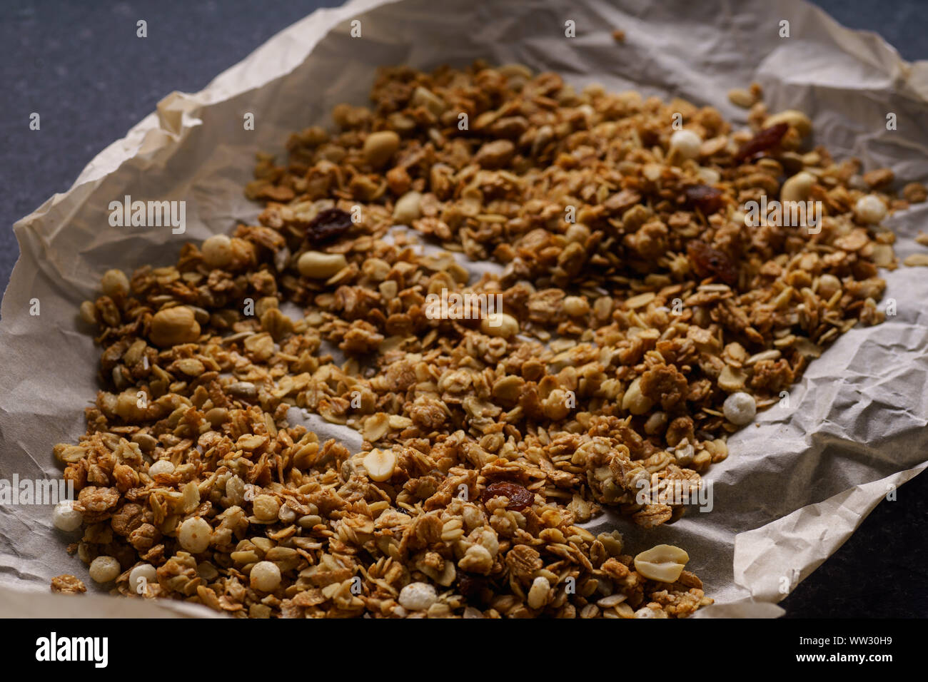 Top view of roasted granola with nuts, flakes and raisins on parchment ...