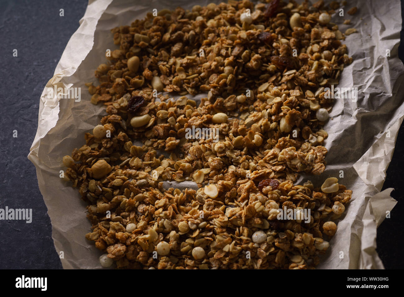Top view of roasted granola with nuts, flakes and raisins on parchment ...