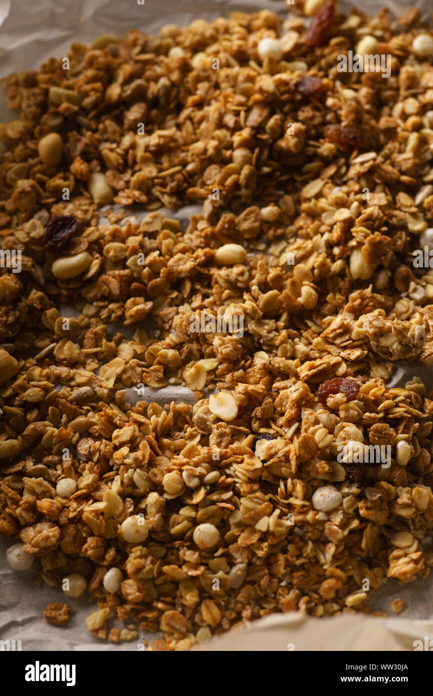 Top view of roasted granola with nuts, flakes and raisins on parchment ...