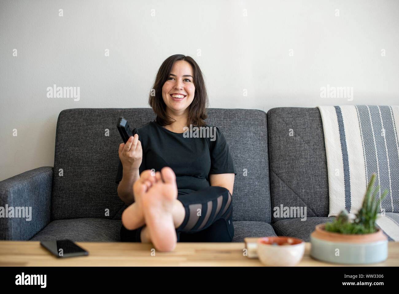 Woman sitting on couch with feet up holding remote Stock Photo - Alamy