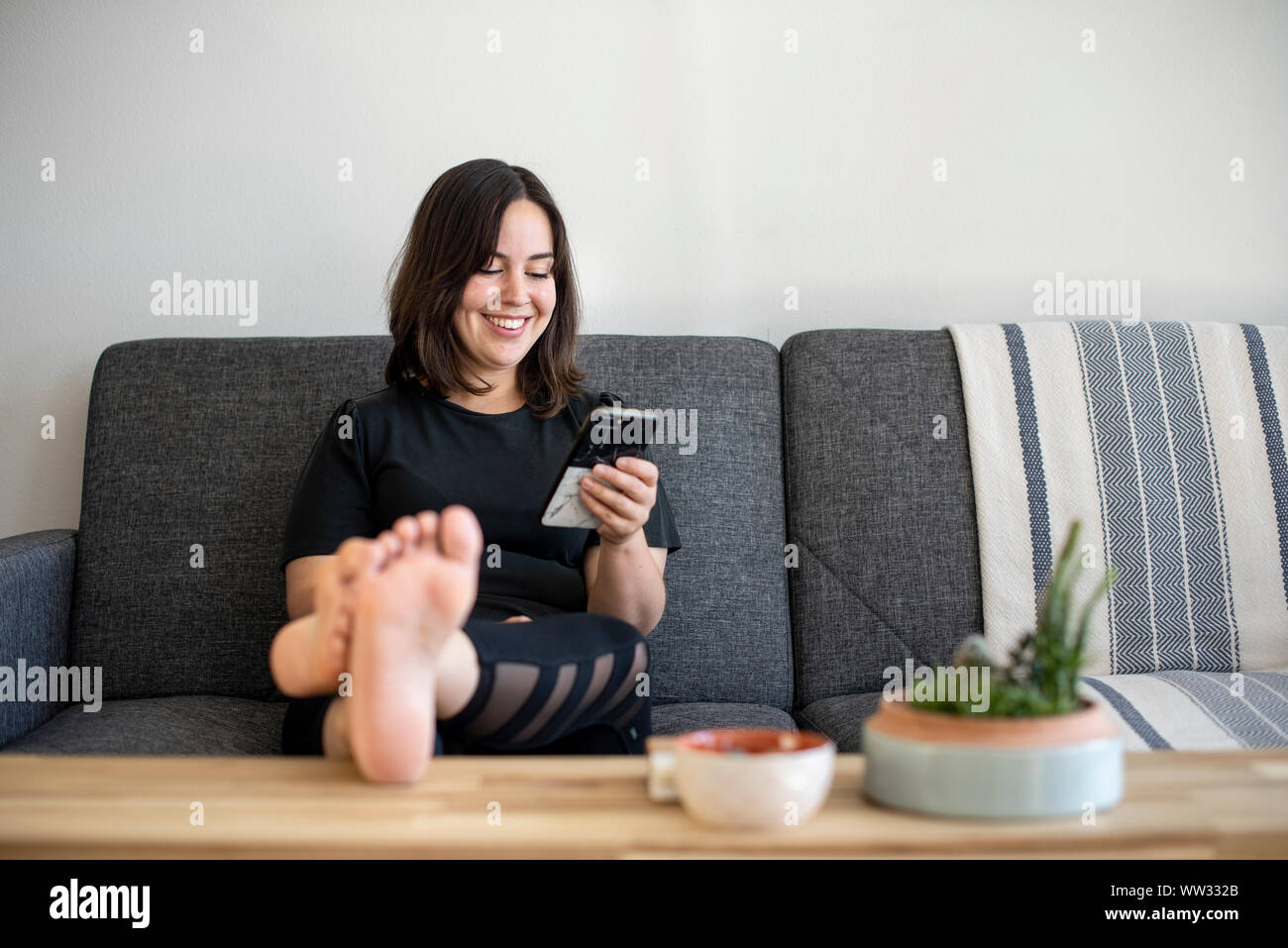 Woman sitting on couch with feet up on phone Stock Photo - Alamy