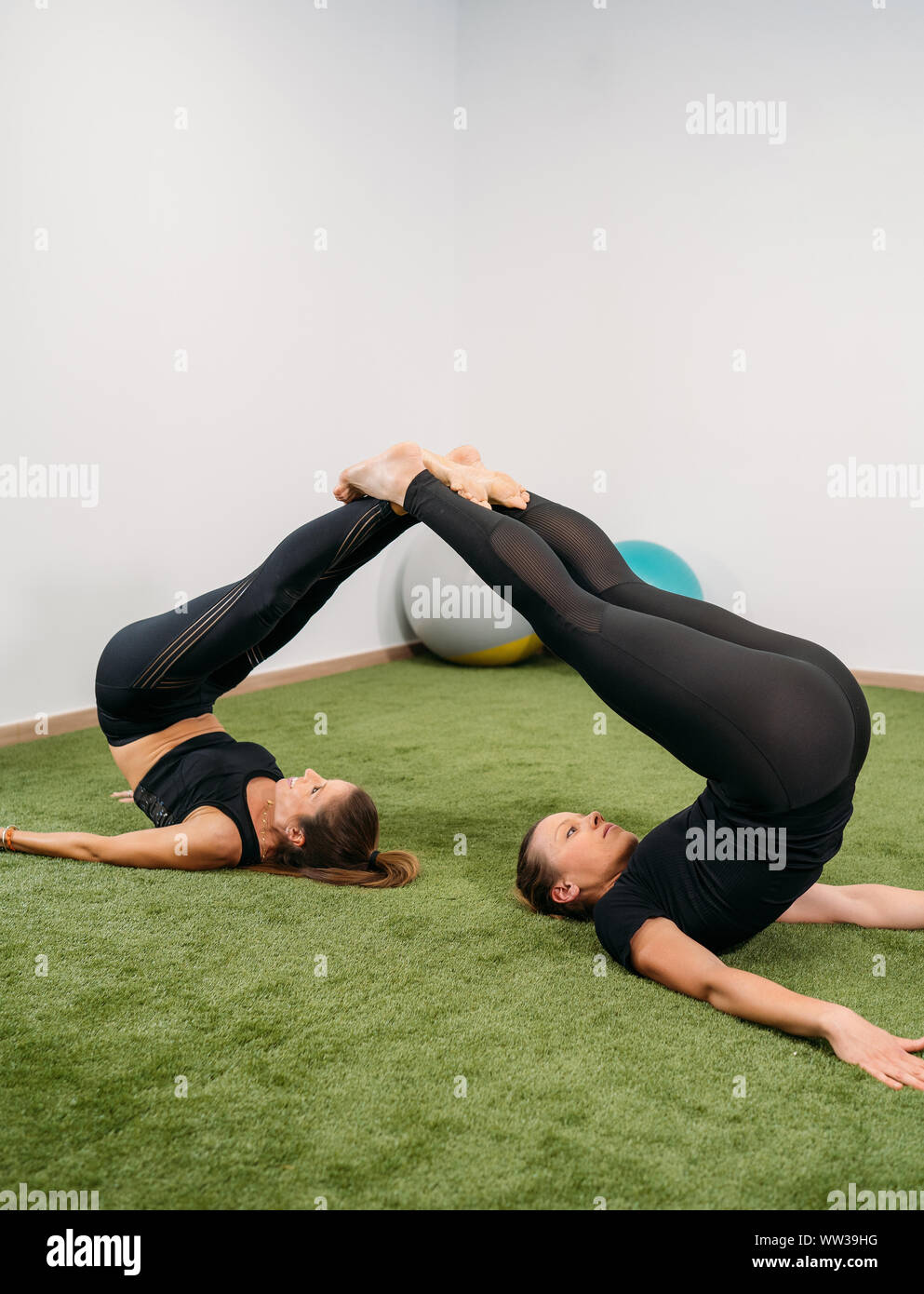Two women dressed in black sportswear join their feet in a stretching ...