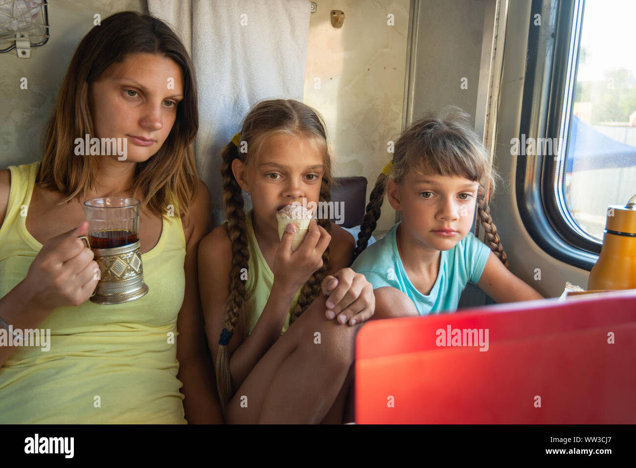 Mom and two girls are looking at the laptop screen in the train car ...
