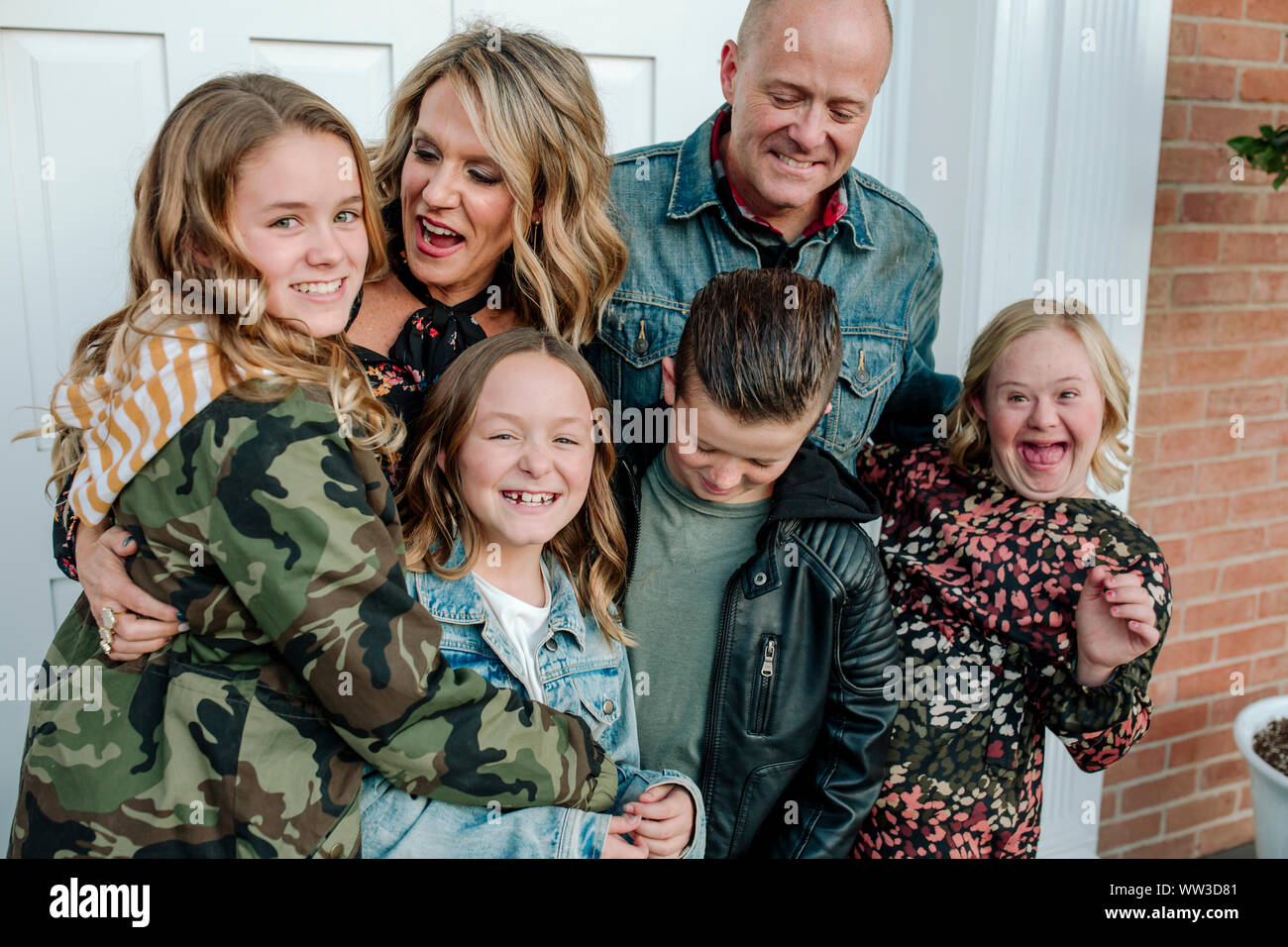 Happy hugging family in front of white door and brick wall Stock Photo ...
