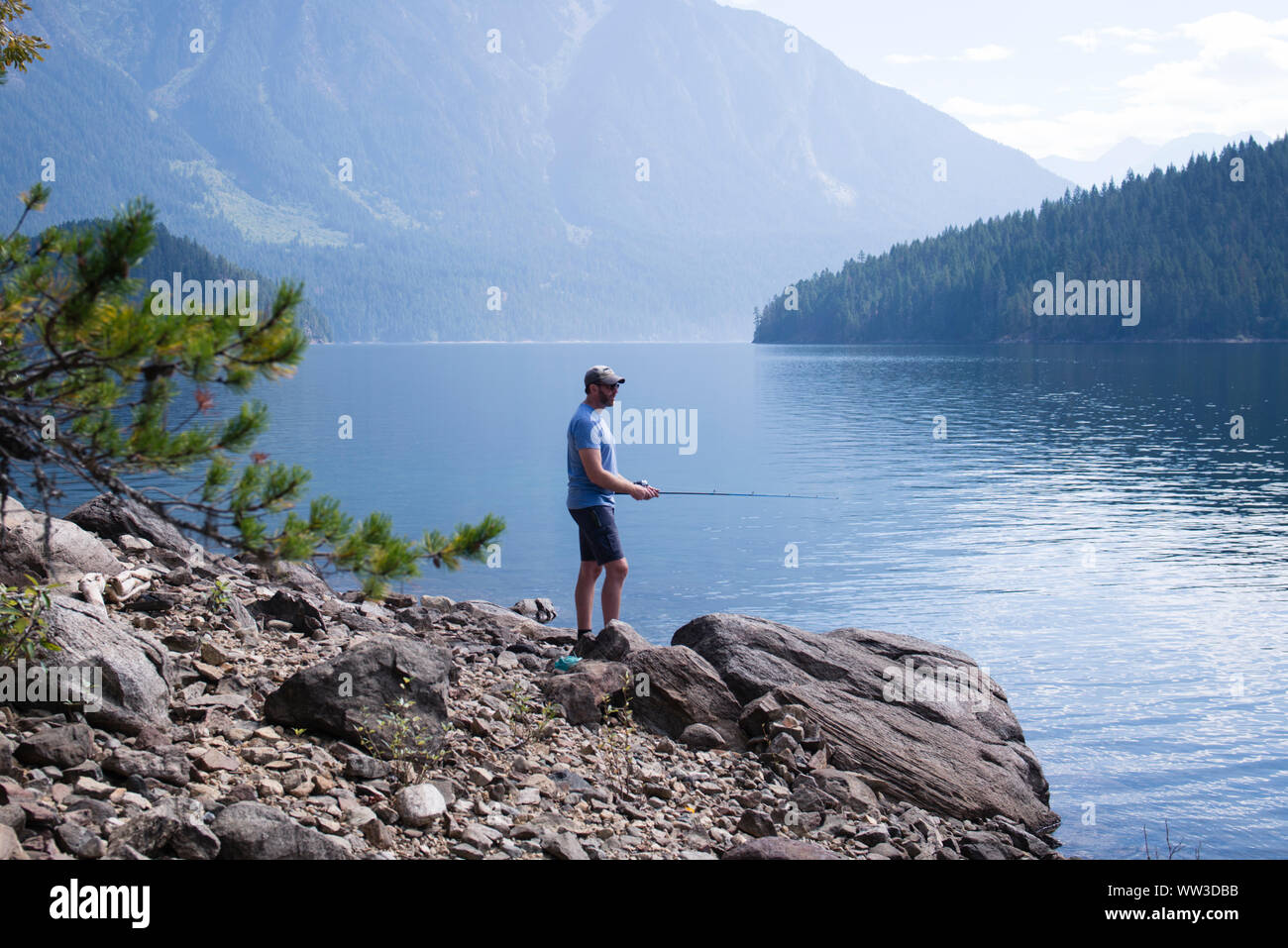 Man Standing on Rocks Fishing at a Mountain Lake Stock Photo - Alamy