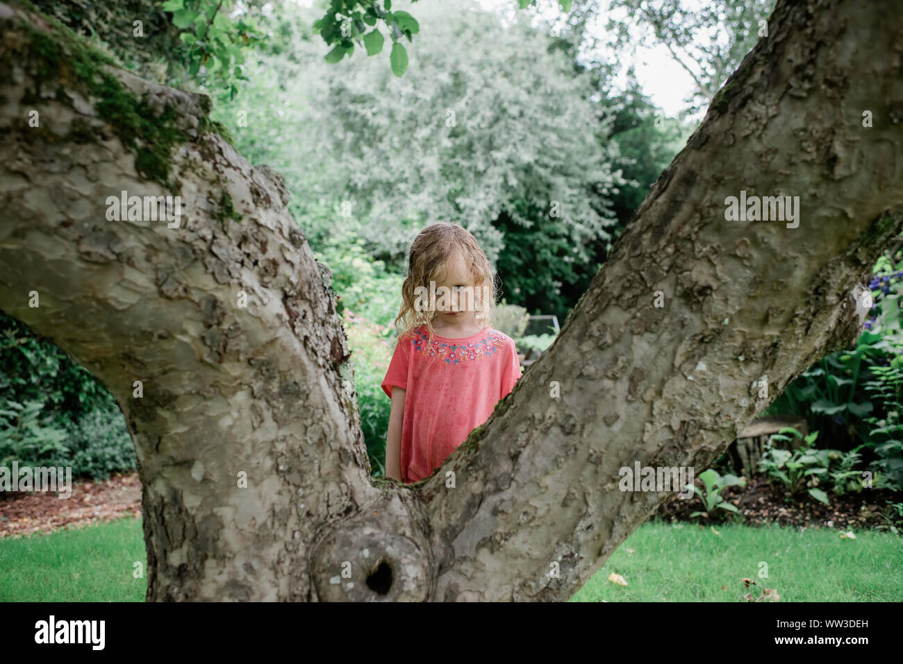 young girl looking sad stood behind a tree in the rain in summer Stock ...
