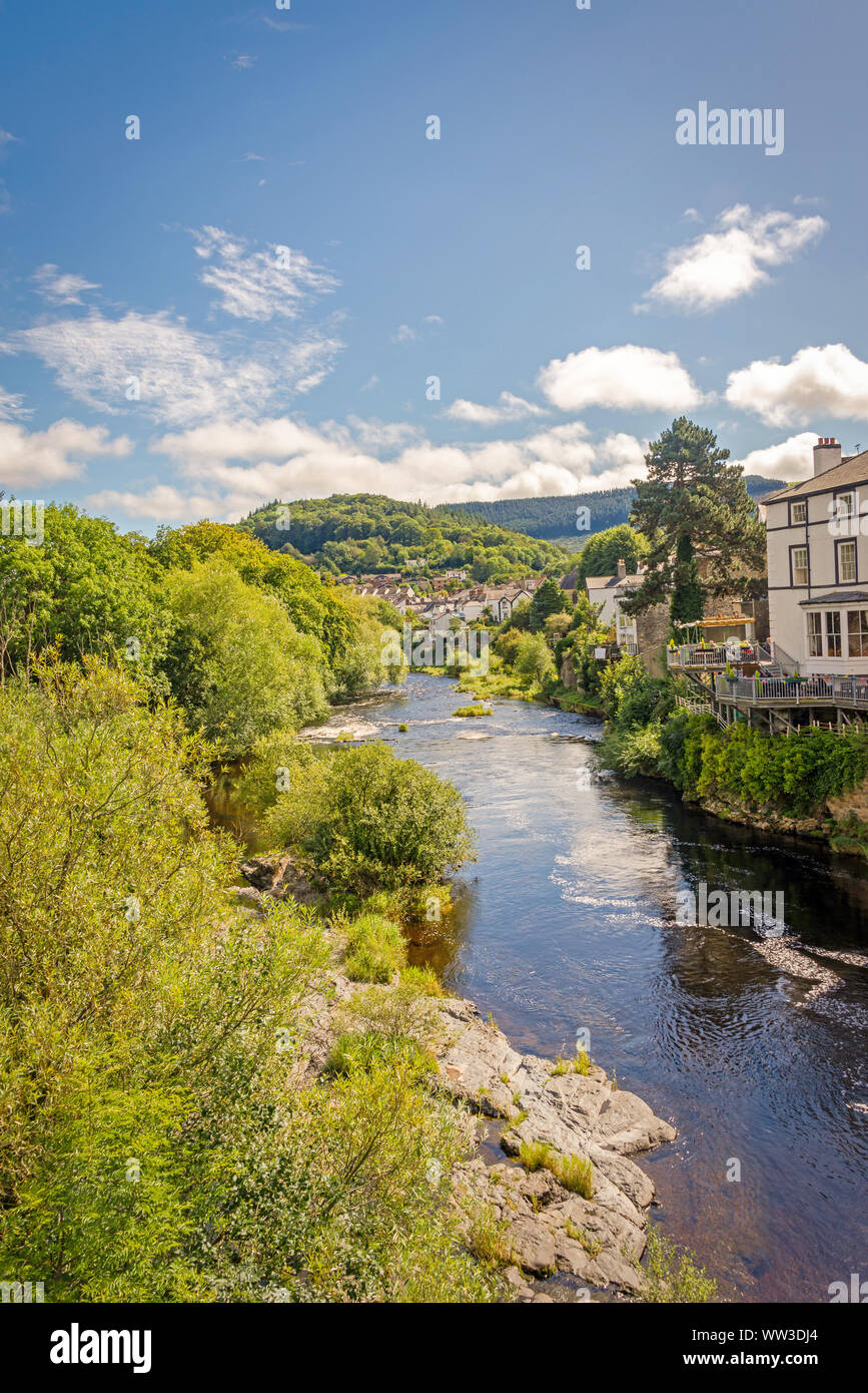 The River Dee at Llangollen beneath a wood covered hill. White coloured ...