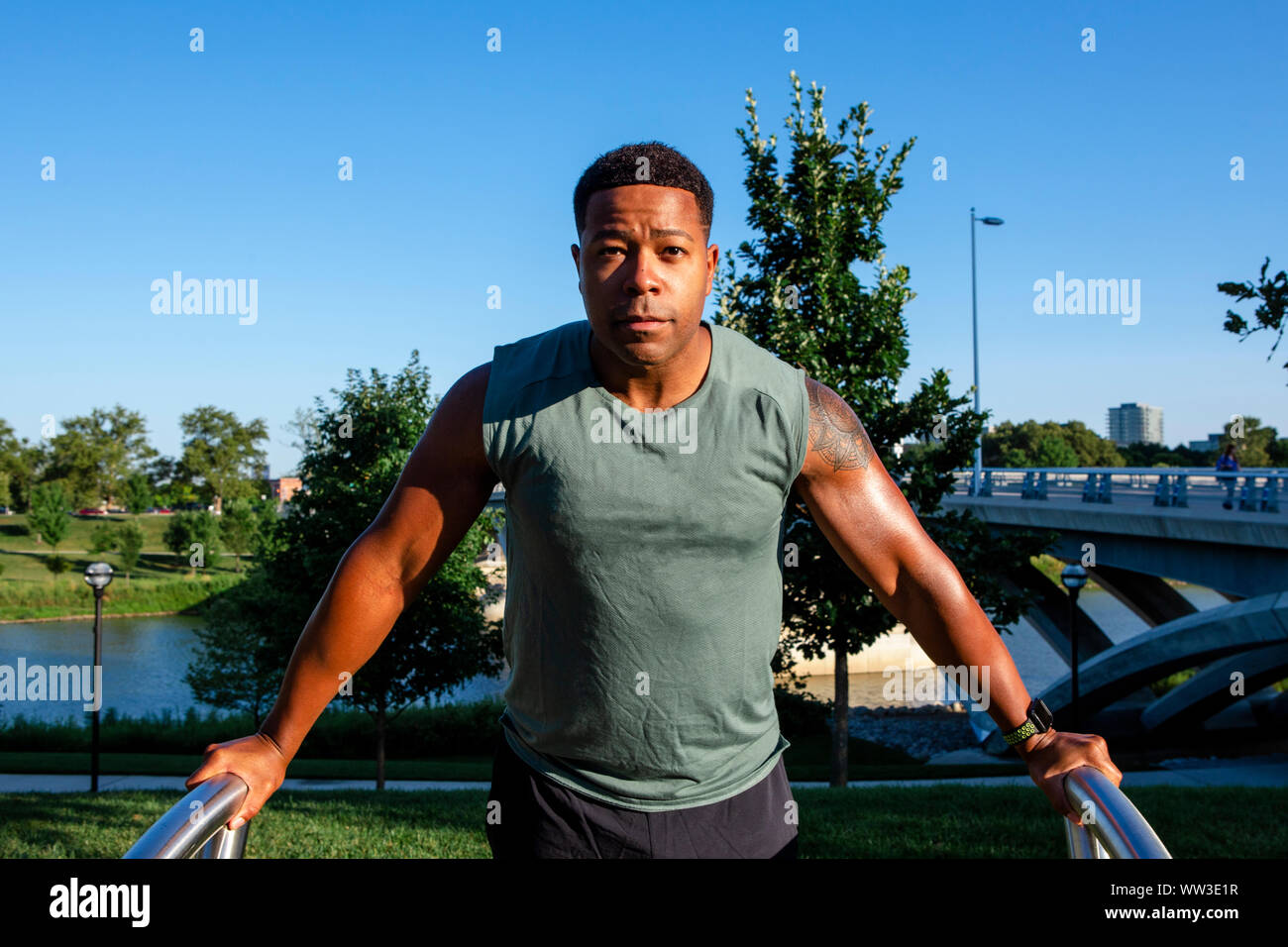 A focused man in athletic gear with direct gaze stretches in a park ...