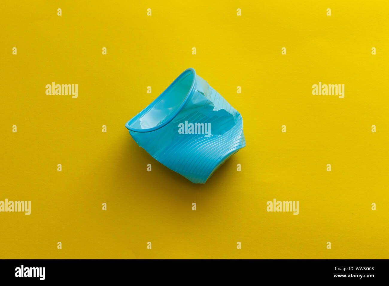 Single broken blue disposable plastic cup over a yellow background ...