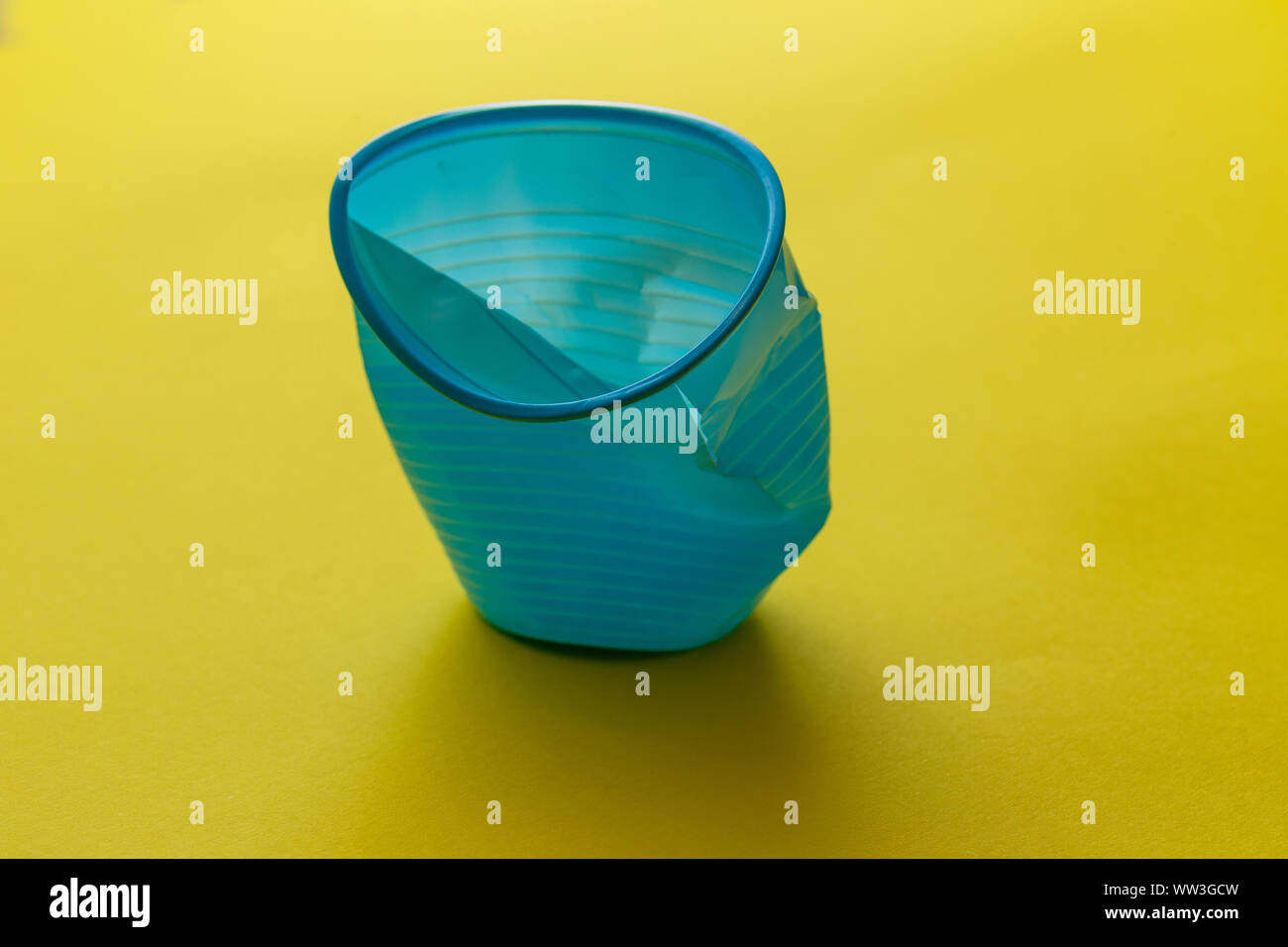 Single broken blue disposable plastic cup over a yellow background ...
