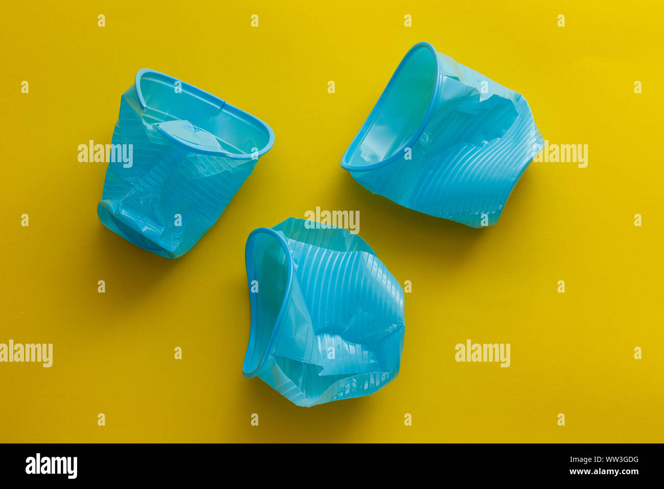 Three broken blue plastic disposable cups over a yellow background ...