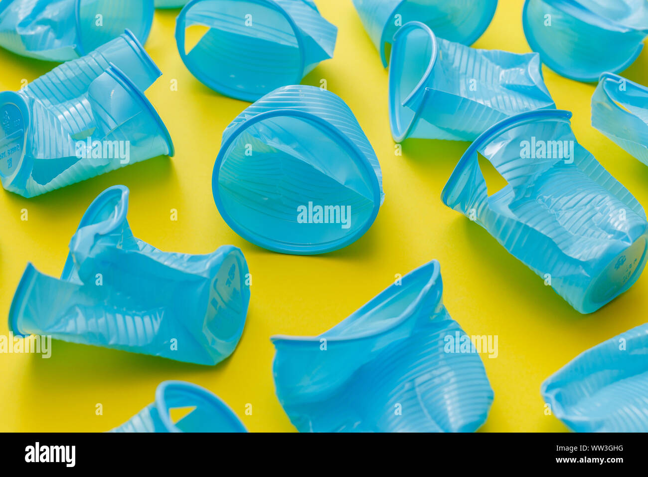 Detail of broken blue plastic disposable cups over a yellow background ...