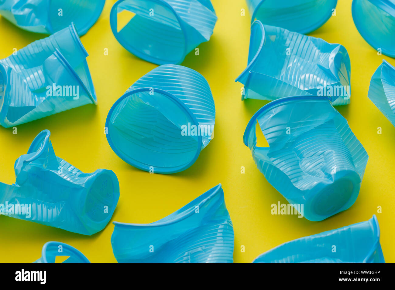 Detail of broken blue plastic disposable cups over a yellow background ...