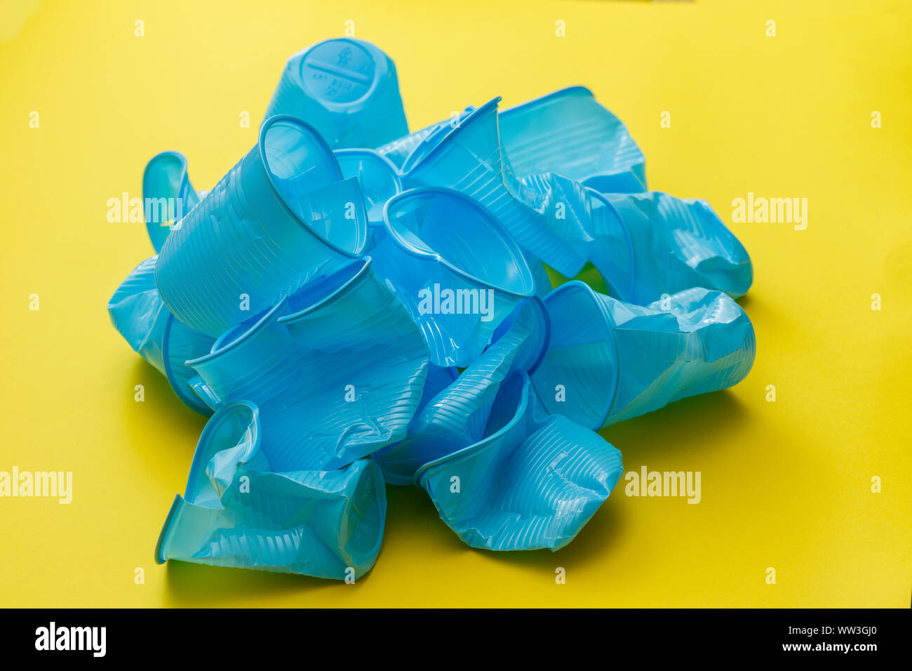 Detail of broken blue plastic disposable cups over a yellow background ...