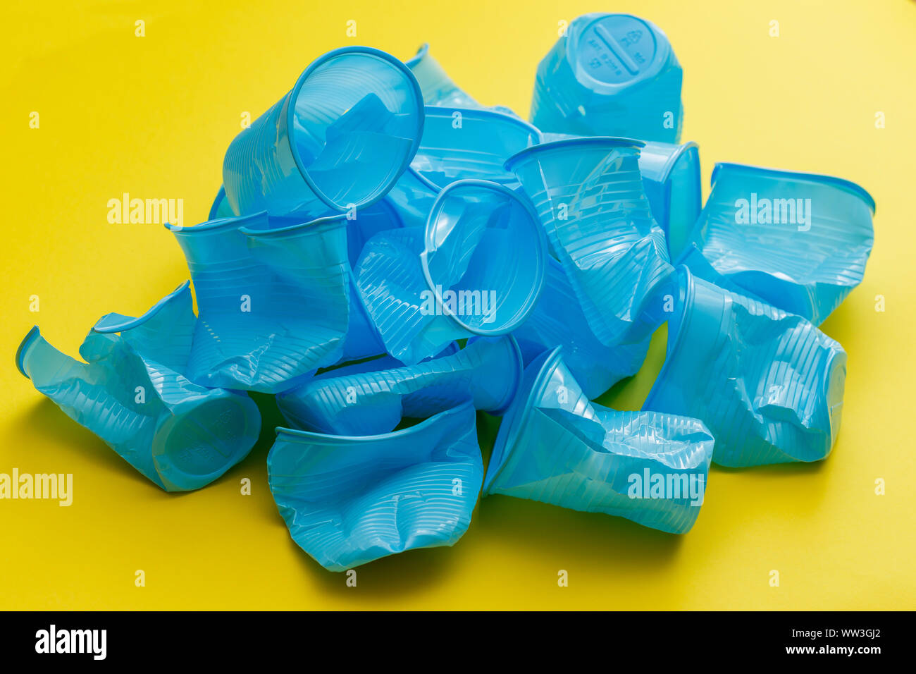 Detail of broken blue plastic disposable cups over a yellow background ...
