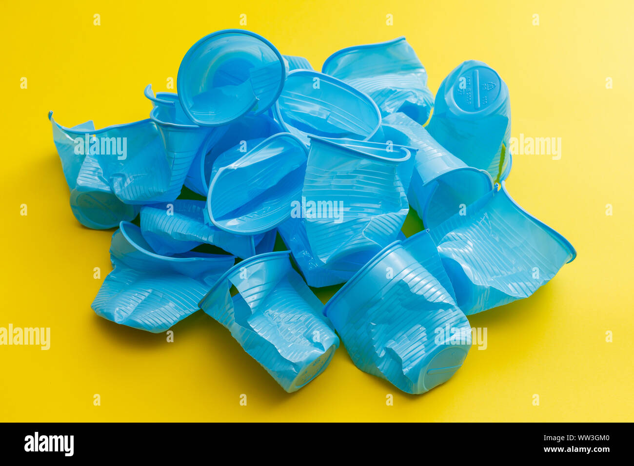 Detail of broken blue plastic disposable cups over a yellow background ...