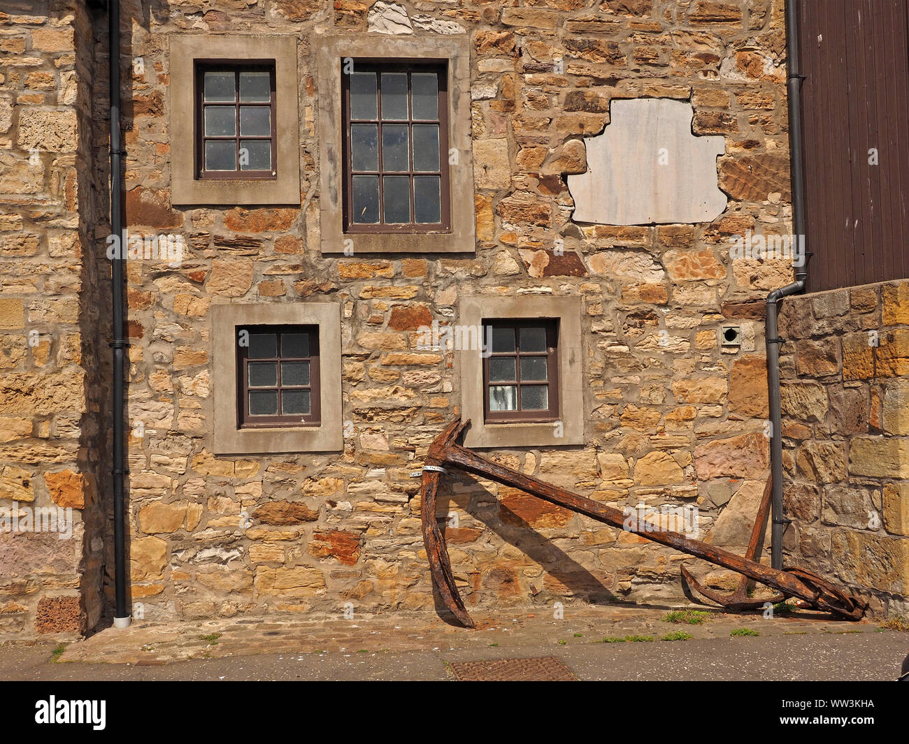 2 large old ships anchors by a stone wall with 4 irregular windows and ...