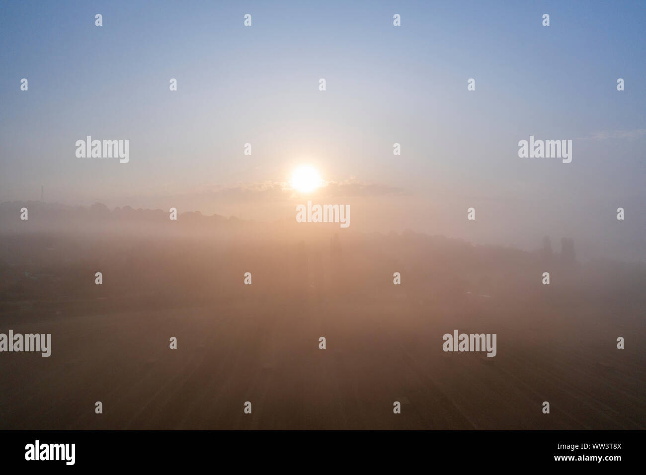 Aerial view over harvest fields with sun breaking through heavy fog at ...