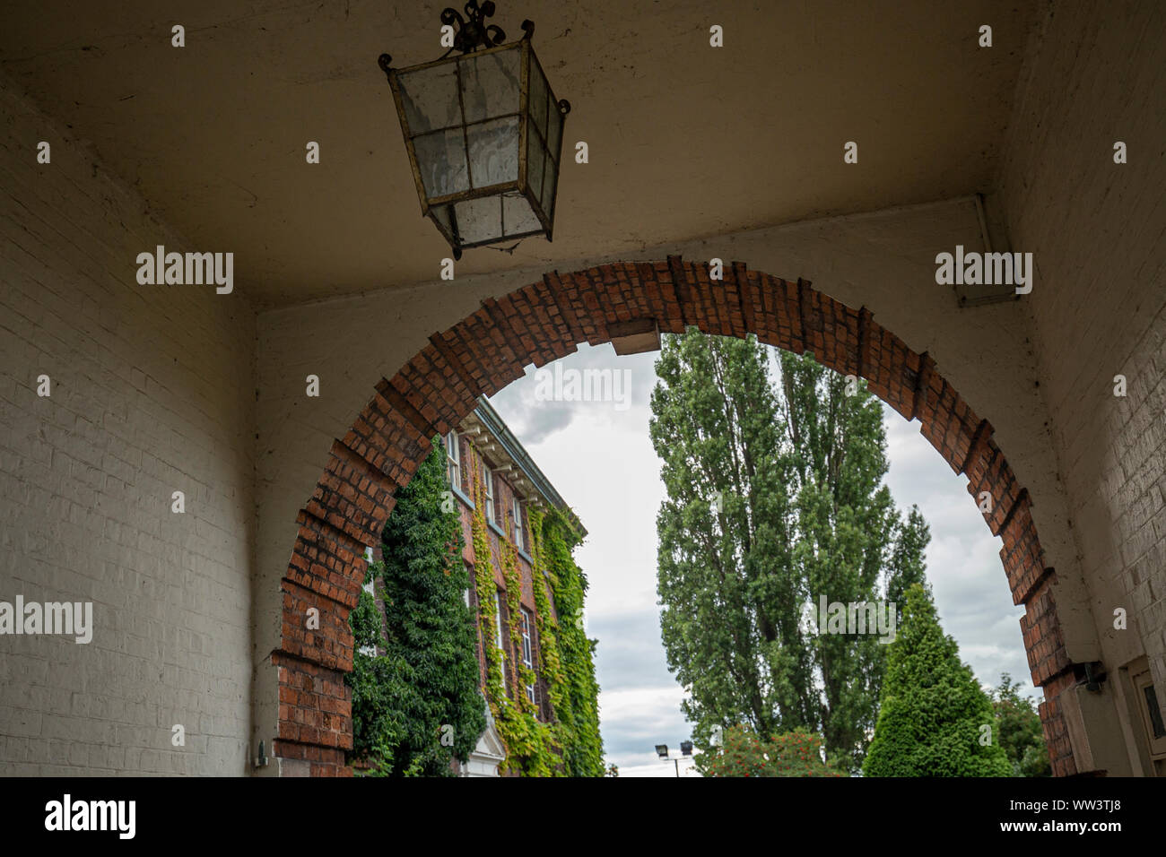Red brick arch entrance into victorian style building with green trees ...