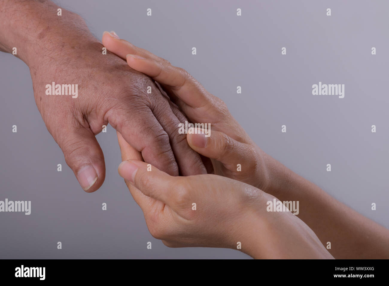 Young woman holding hand of her grandfather over grey background ...