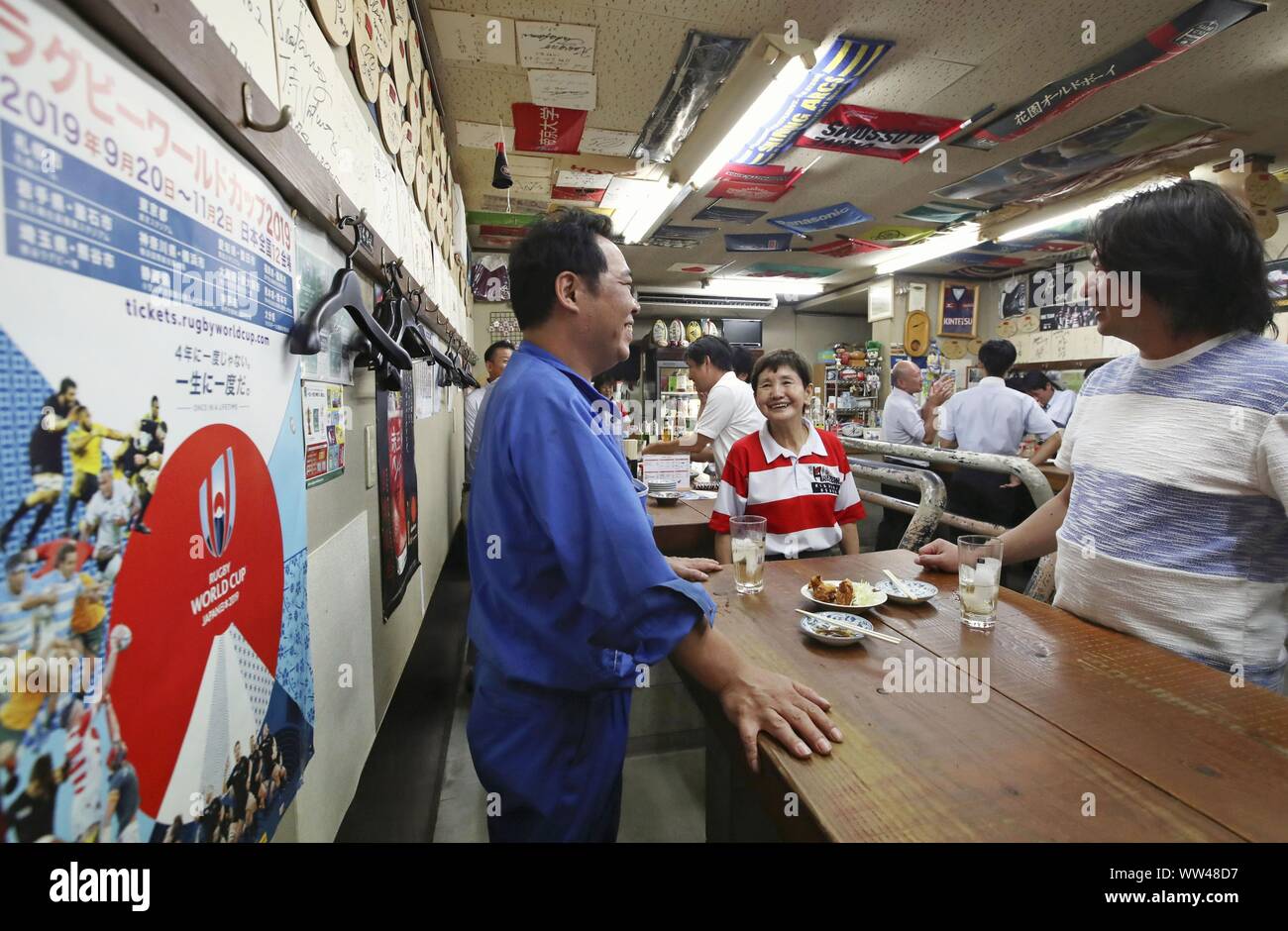 Bar master Asako Azumaya, wearing a rugby jersey, chats with customers ...