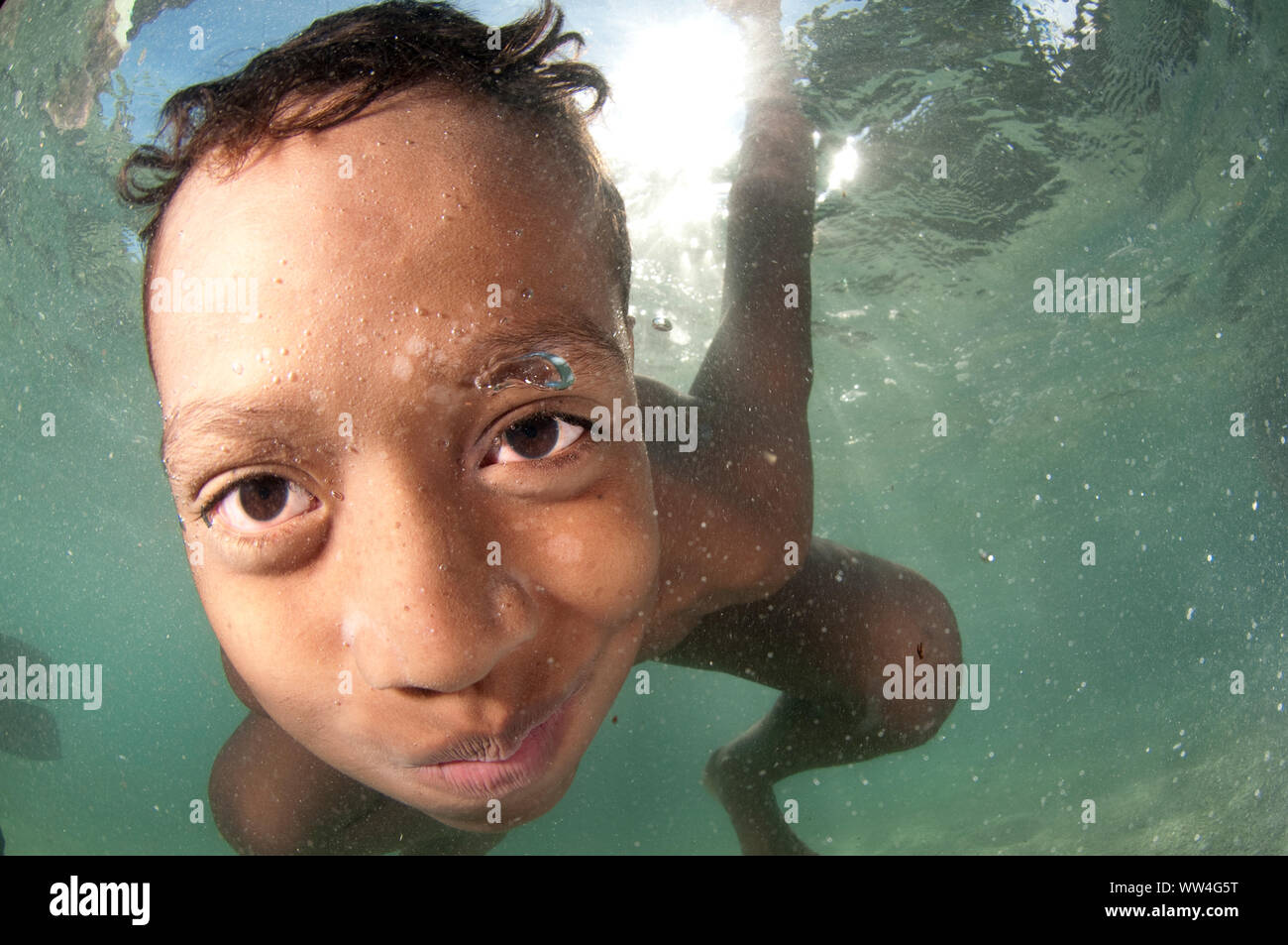 Boys playing, underwater in shallow water with sun in background, Ambon ...