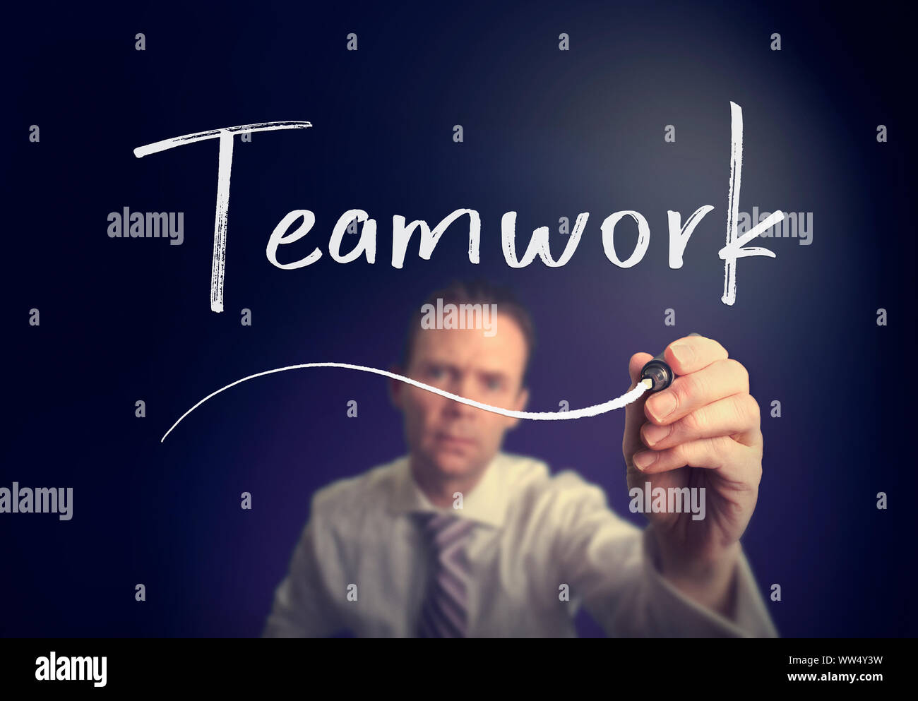 A businessman writing a Teamwork concept with a white pen on a clear ...