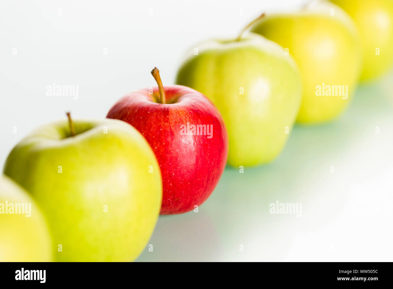Red apple standing out from row of green apples Stock Photo - Alamy