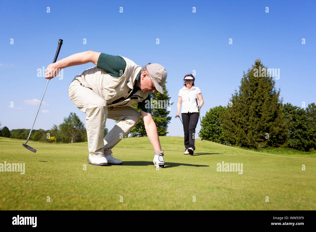 Golf player couple on green picking ball Stock Photo - Alamy