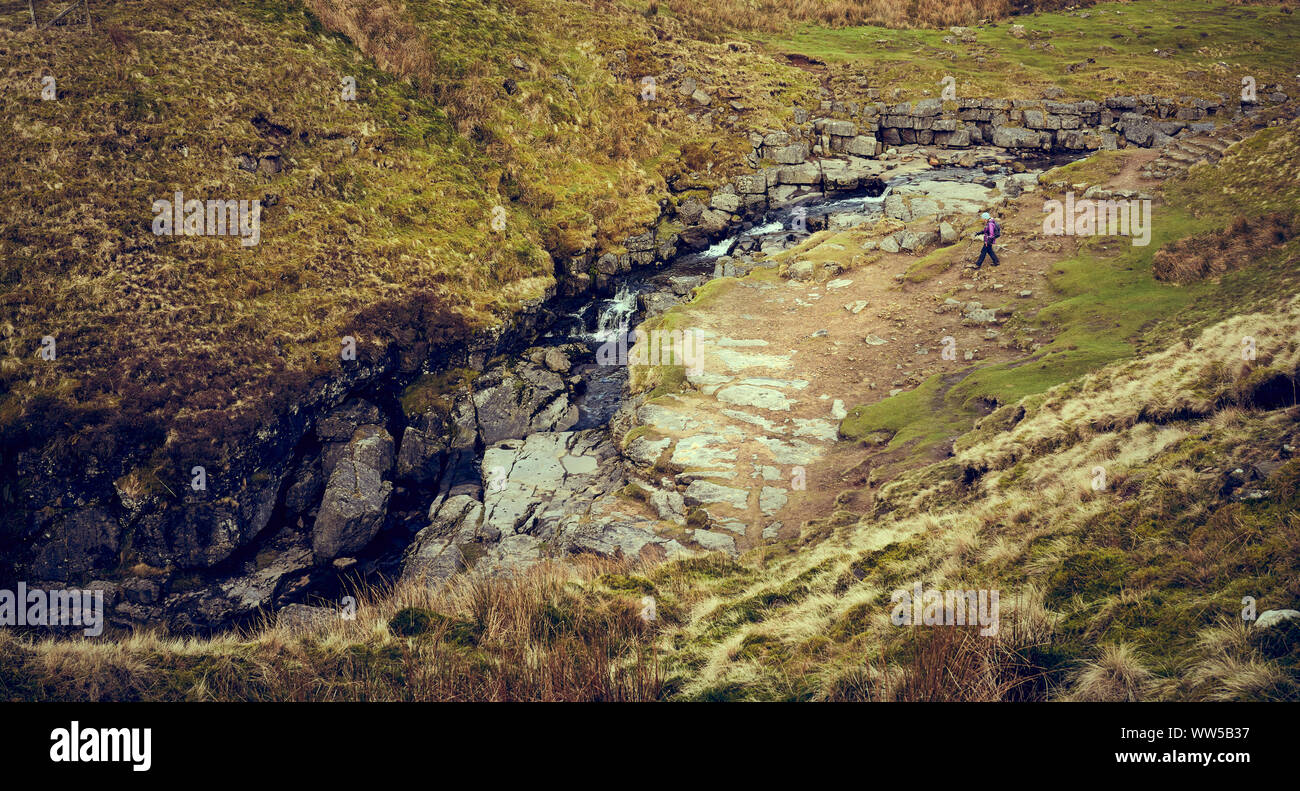 A distant hiker at the entrance to Gaping Gill Cave in the limestone ...