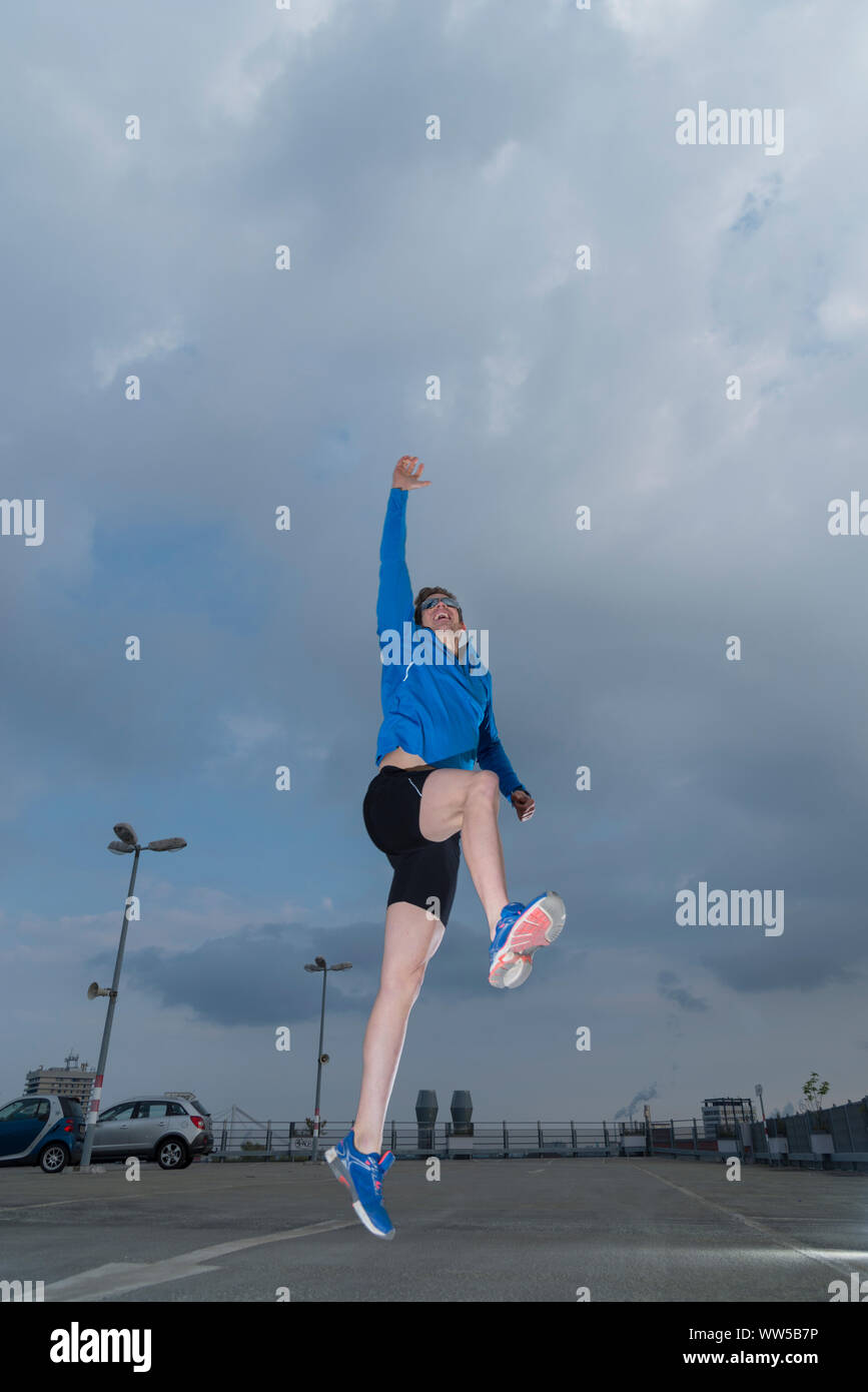 Man in blue tracksuit top, jumping, arm upwards Stock Photo - Alamy