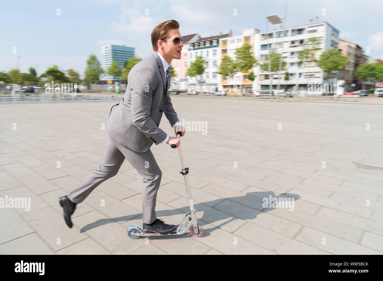 Man in grey suit riding scooter on town square hi-res stock photography ...