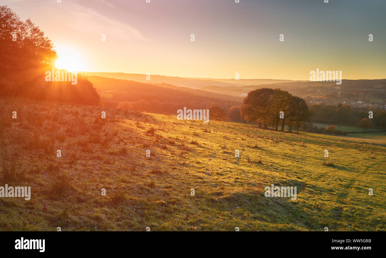 Red, Orange and yellow glow of a sunset over green pastures and trees ...