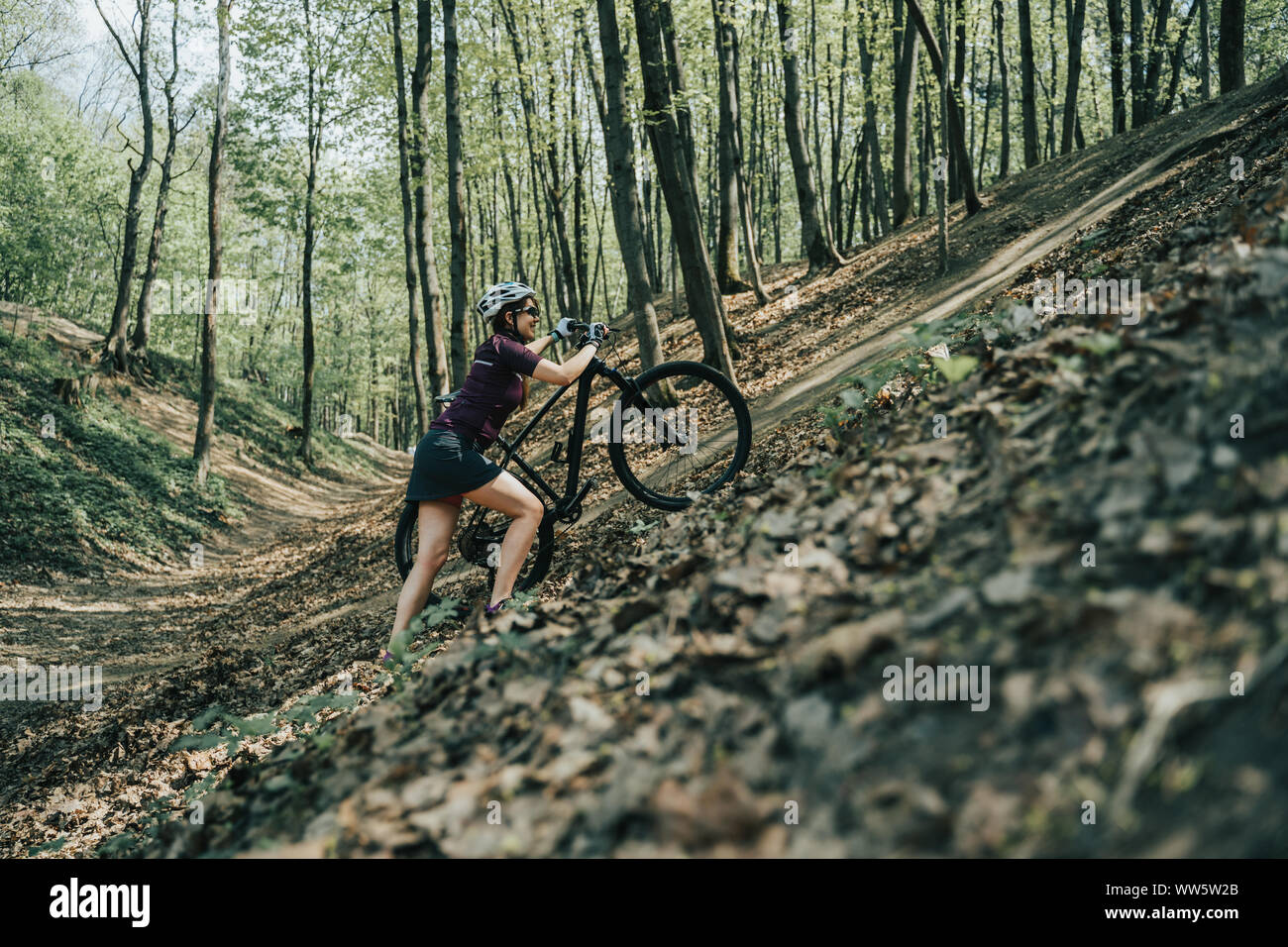 Photo of female athlete in helmet raising bicycle to hill in forest on ...