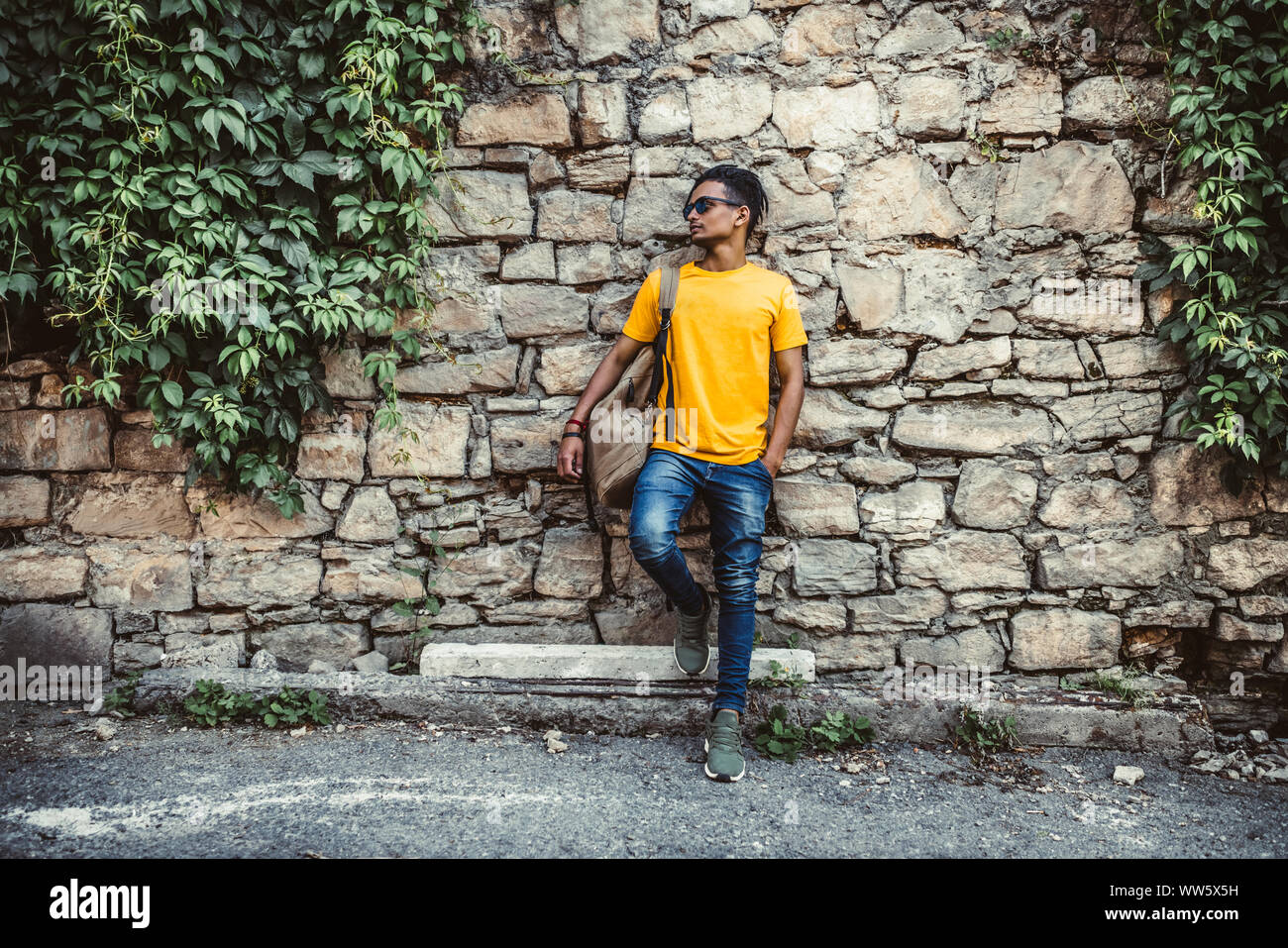 A young Indian man stands near the stone wall. Trendy and fashionable ...