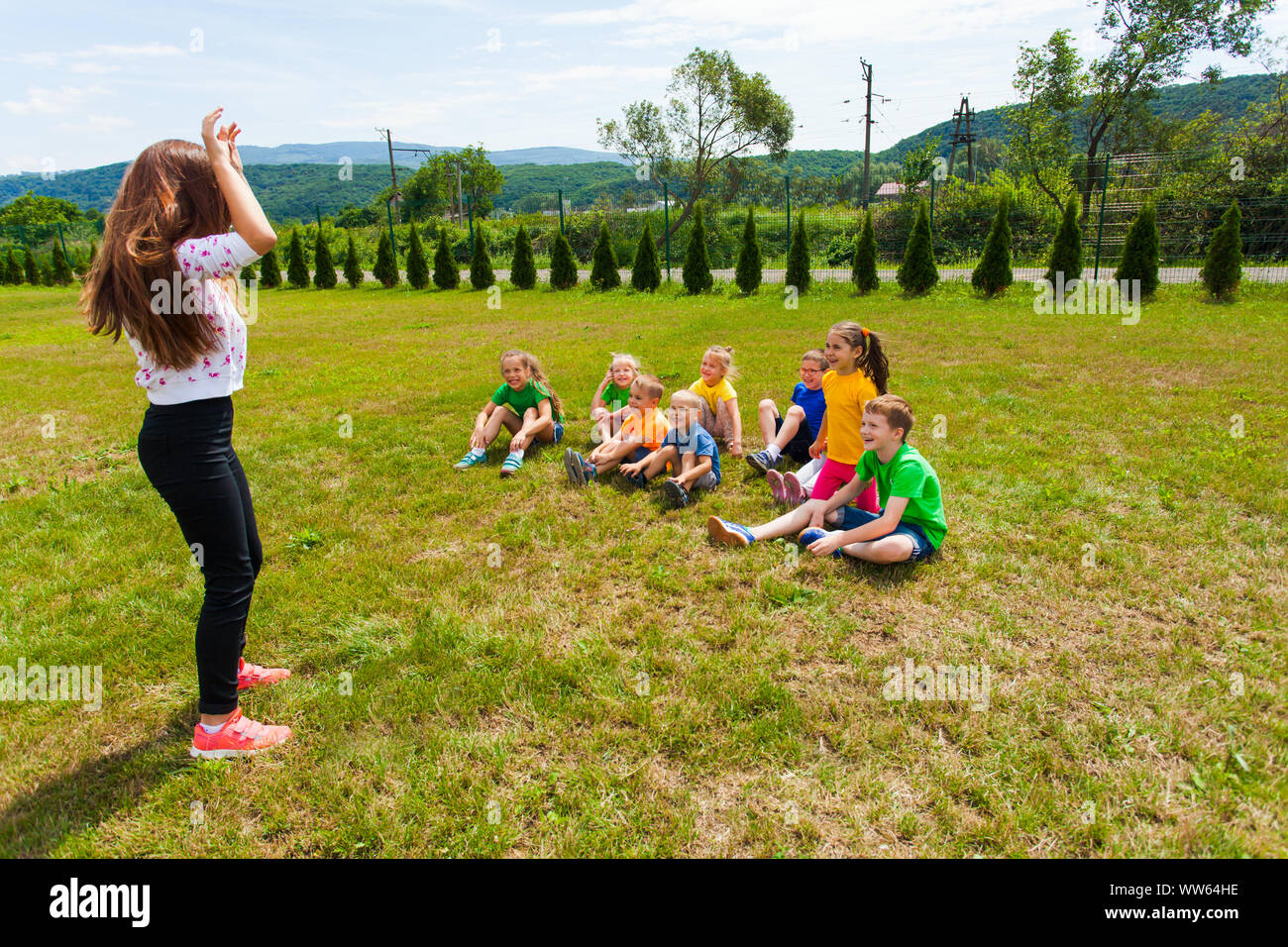 Young girl camp leader playing charades with group of preschoolers in ...