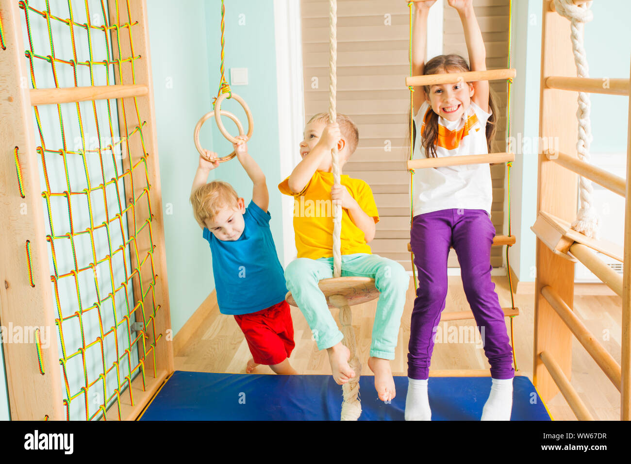 Three active children of different age climbing up the wooden rope ...