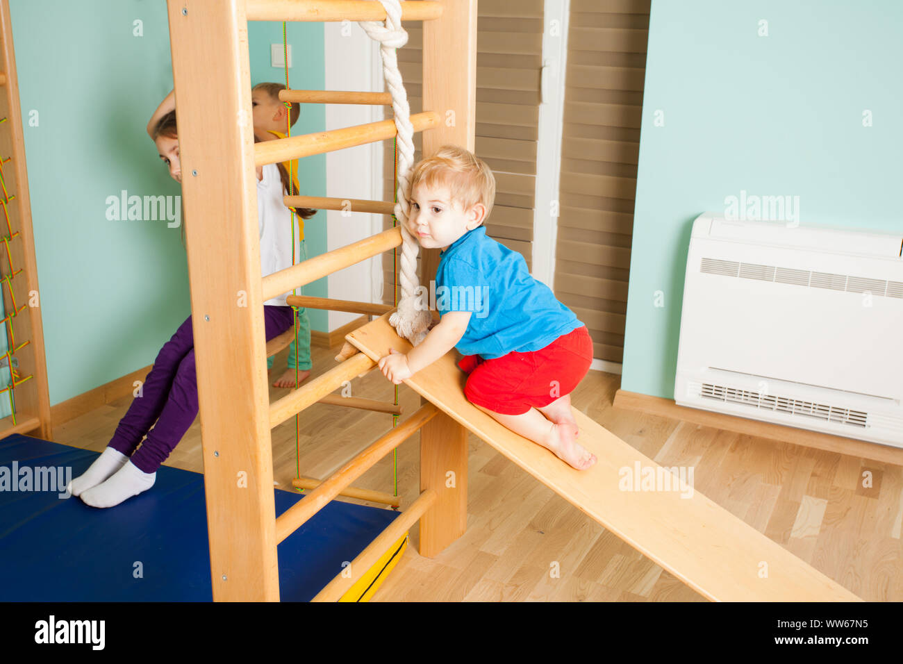 Cute little boy barefoot in a blue t-shirt climbing up the wooden slide ...